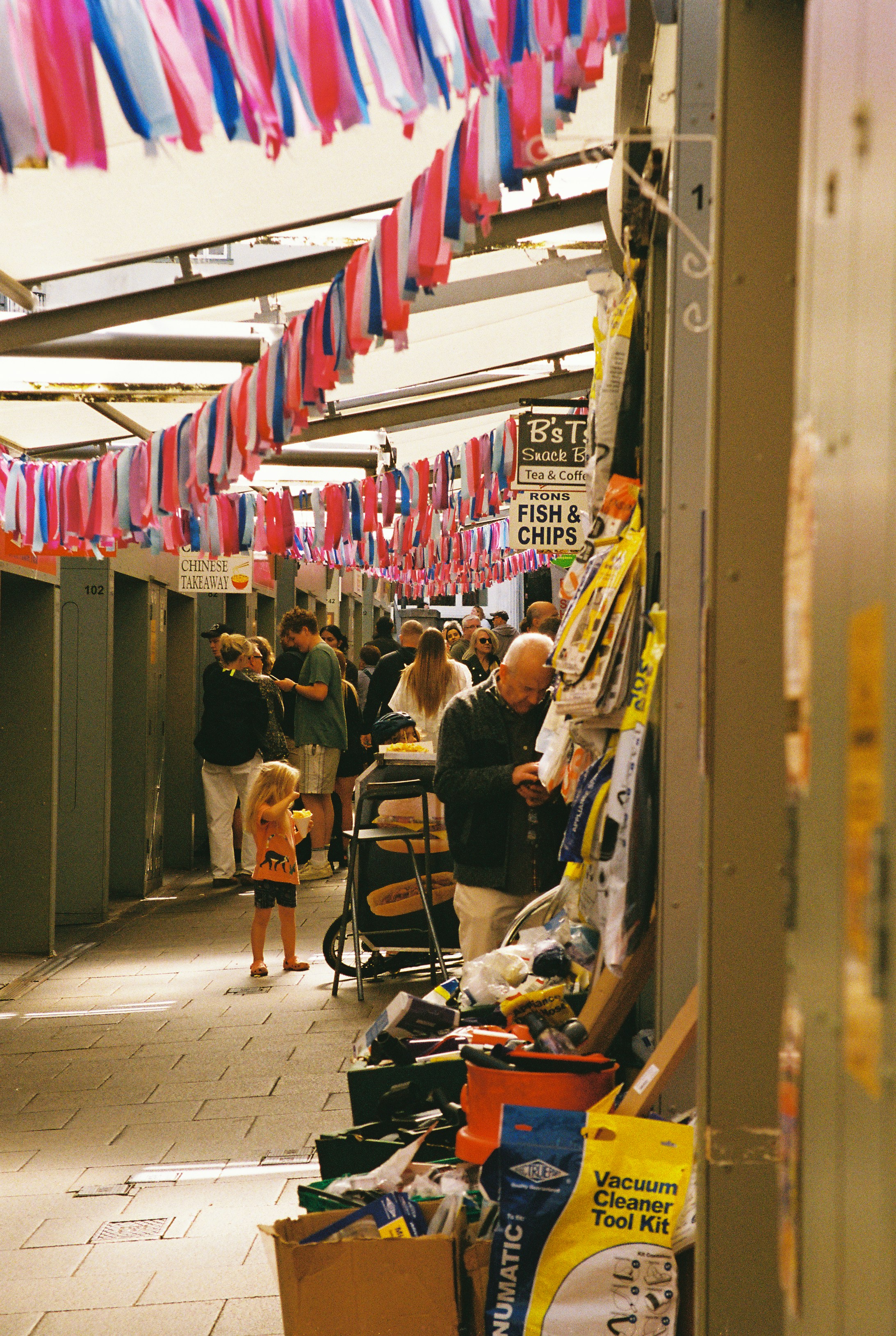 Colorful Market Corridor: Streamers, Shoppers, and a Child's Curious Gaze