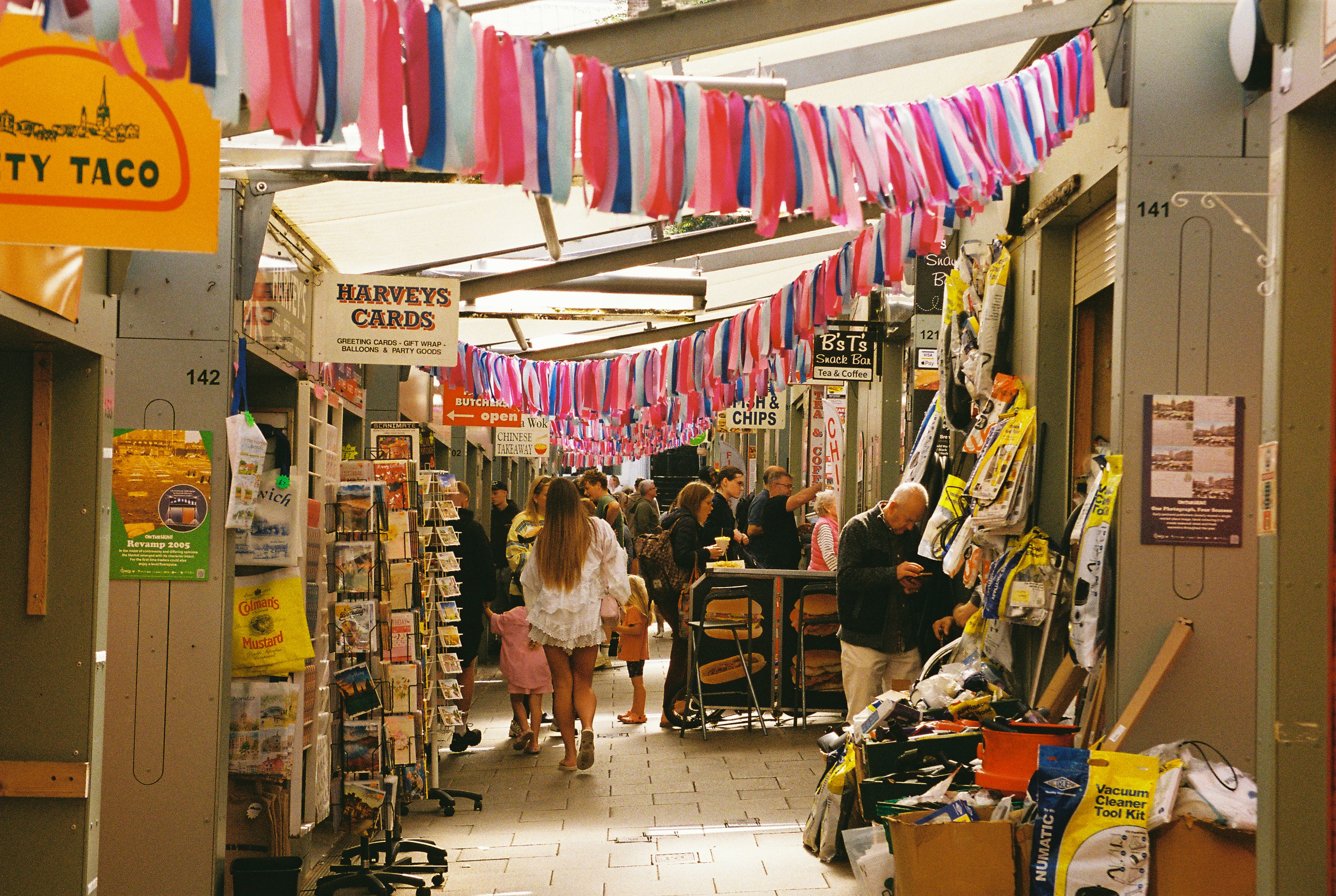 Colorful Market Corridor with Shoppers and Stalls Under Festive Banners