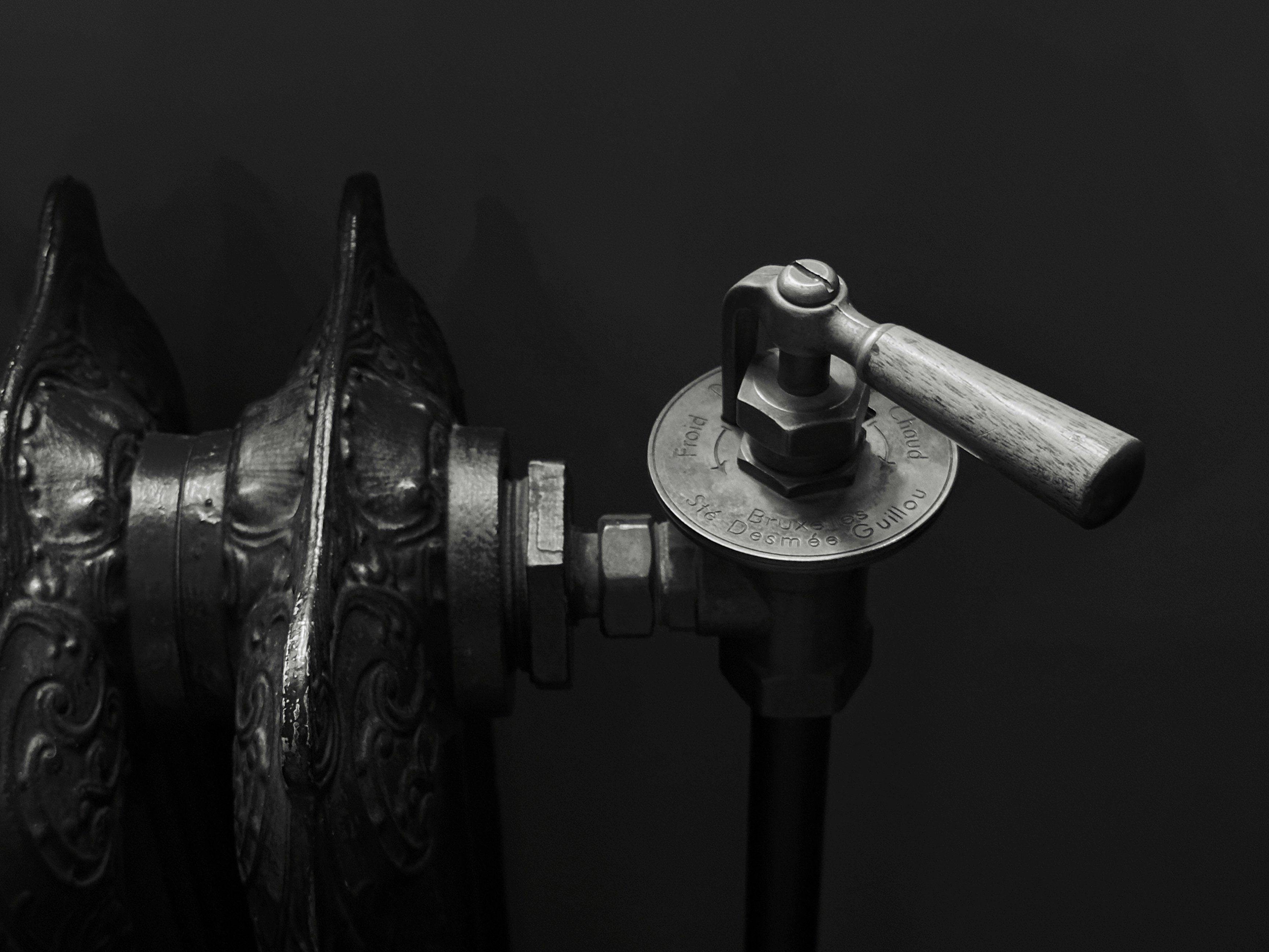 A close-up of an ornate vintage stop valve against a dark background, highlighting textured metalwork and contrast. The scene emphasizes craftsmanship and the functional detail of the hardware.