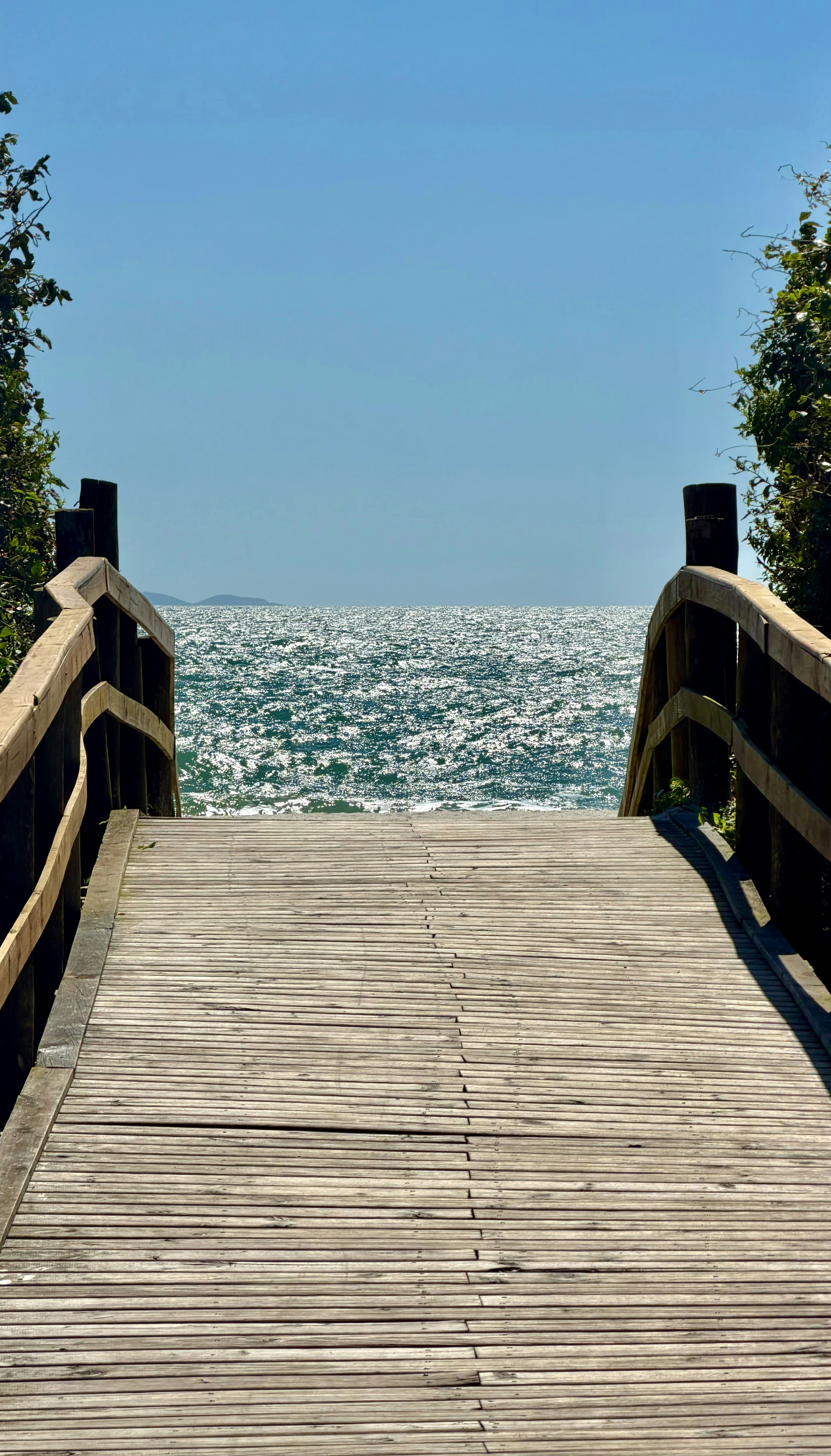 A wooden footbridge leading to the sparkling blue ocean under a clear sky