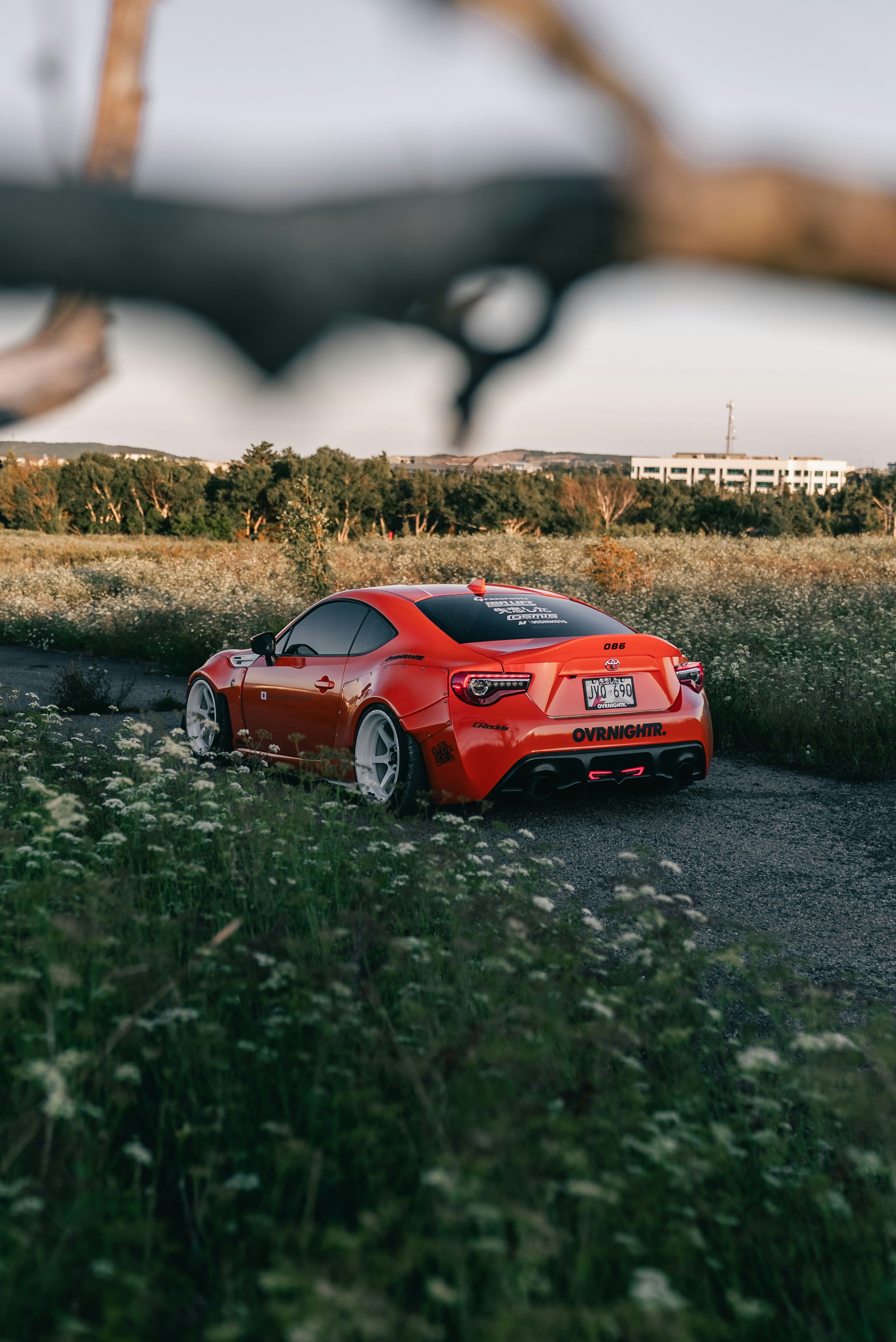 Red Coupe in a Wildflower Field with a Hovering Drone Shadow