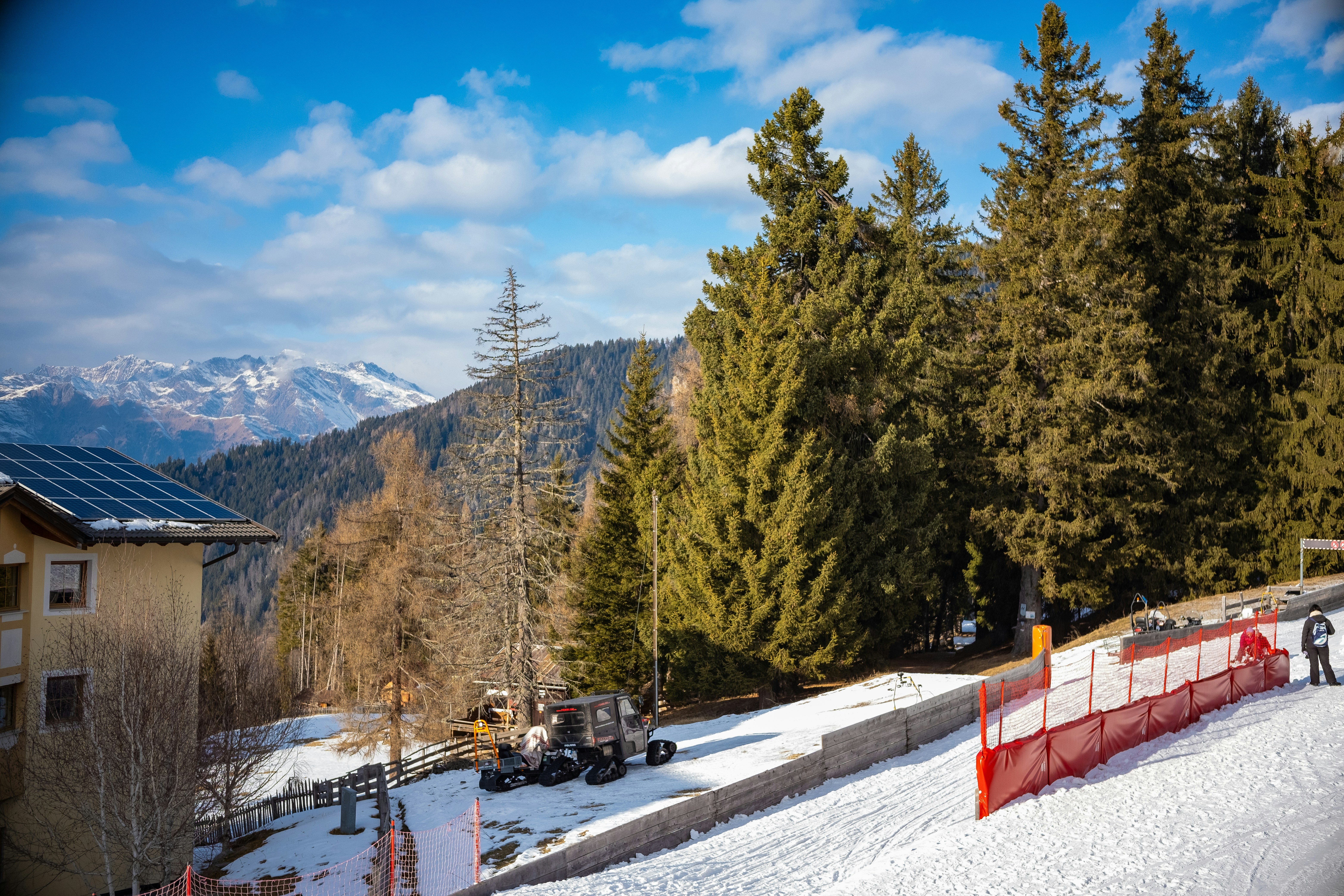 Snowy slope under pines with distant mountains and crowd-controlled fencing