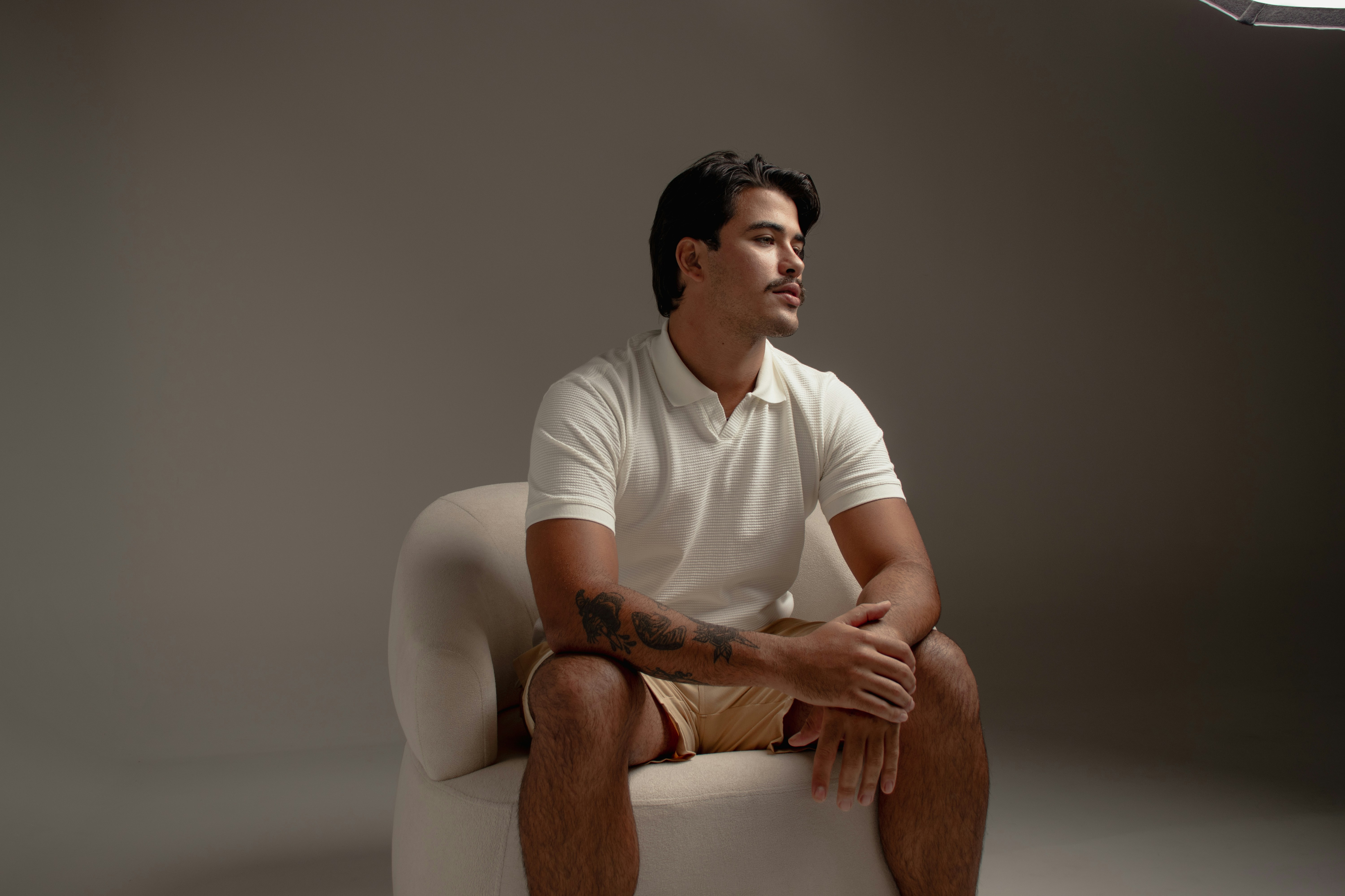 A man with tattoos on his arm wearing a white polo shirt in a chair