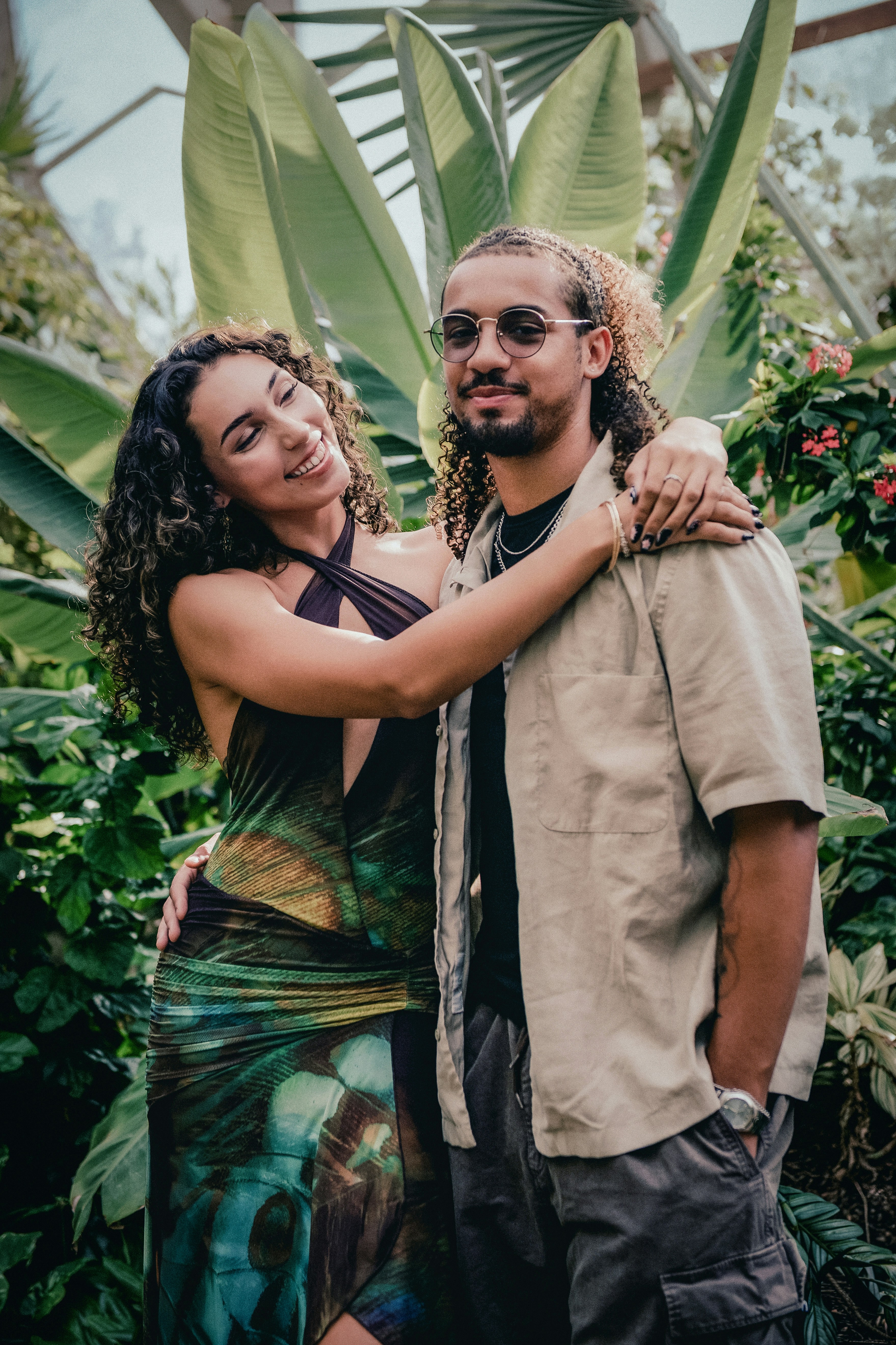 Two friends in a sunlit garden share a warm embrace amid tropical greenery