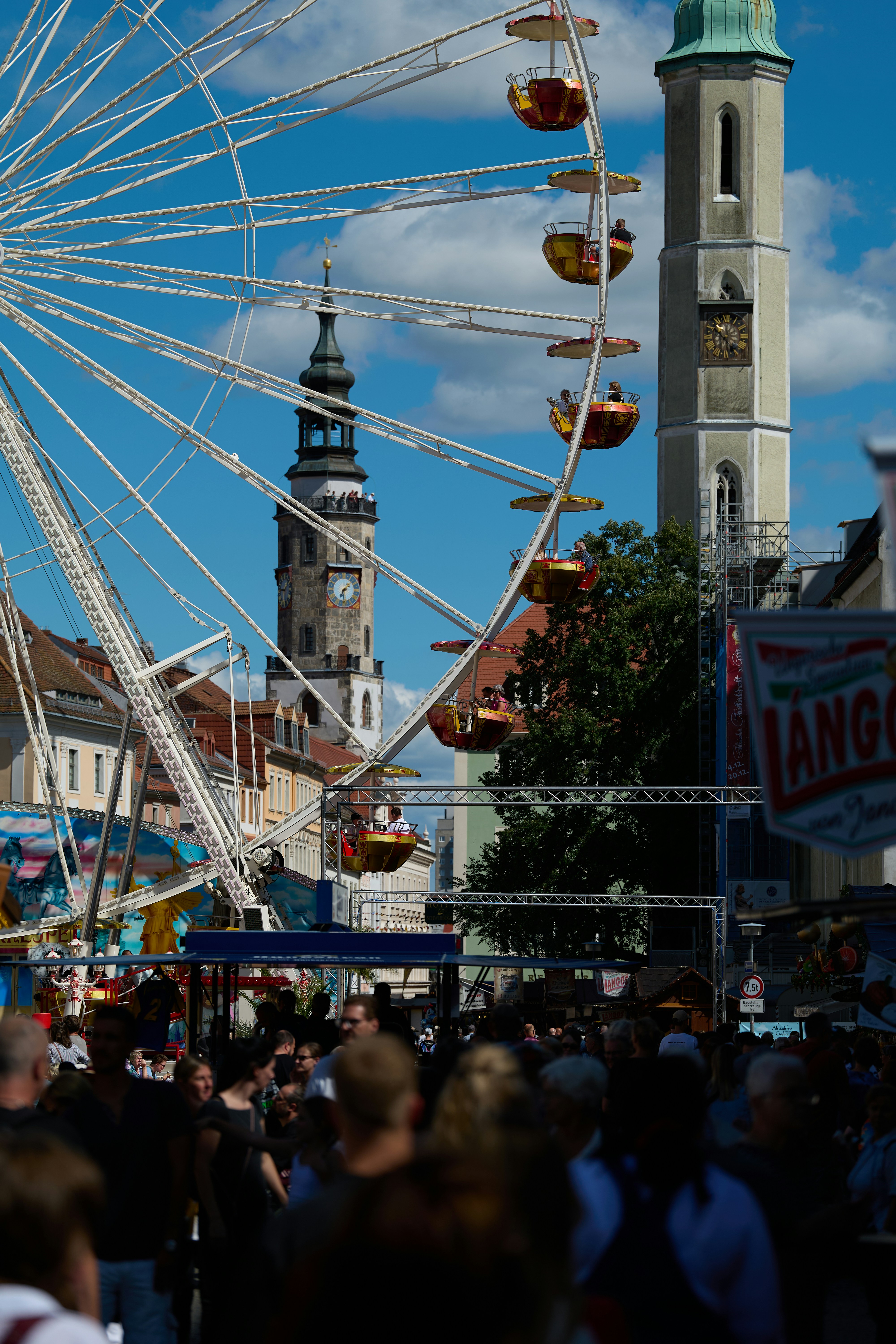 Ferris wheel at a summer city fair with historic church towers in the background, crowd below, Görlitz Germany