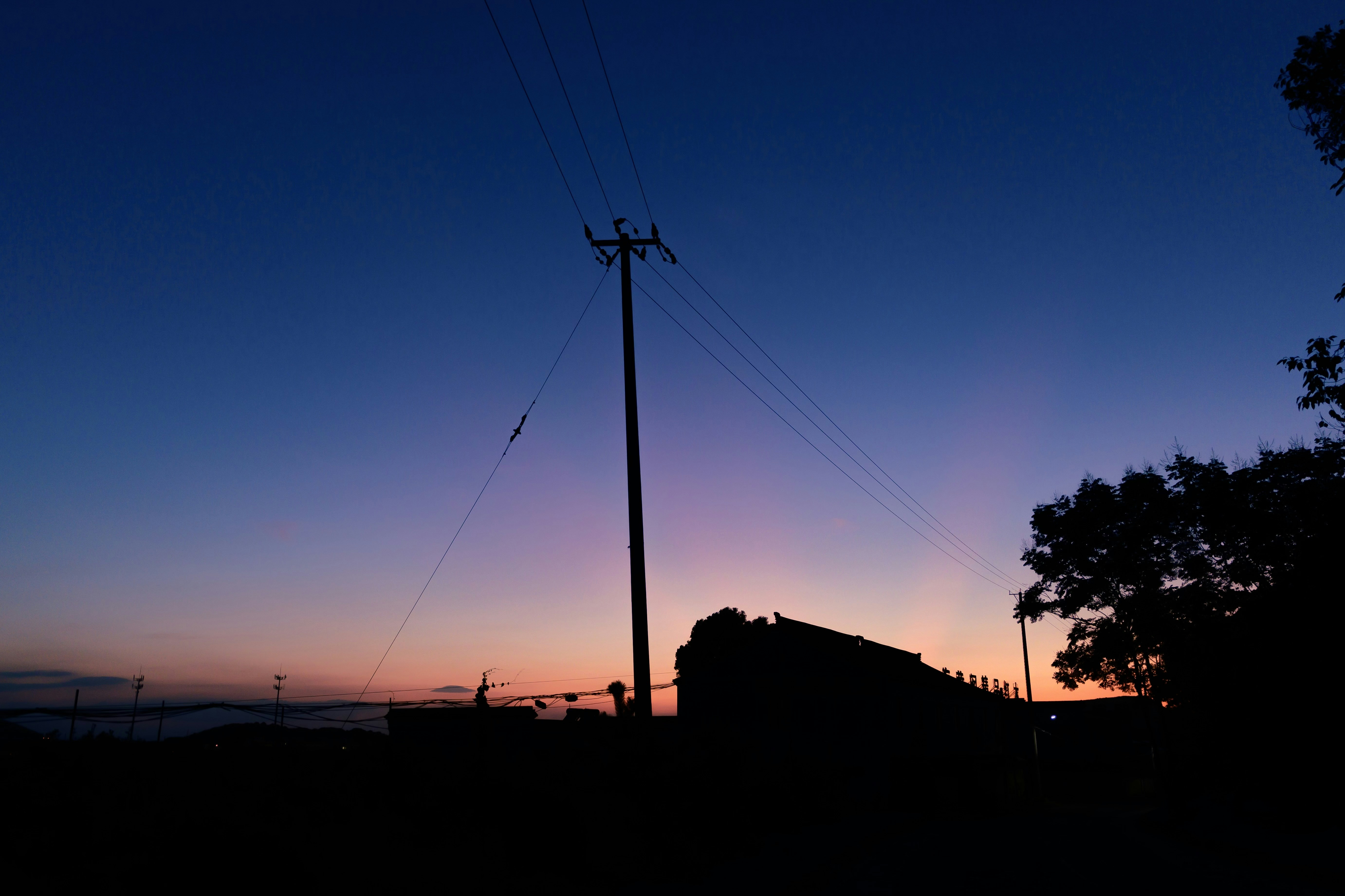 Silhouetted buildings and utility pole against a gradient sunset sky, with low foreground darkness and warm orange-pink glow.