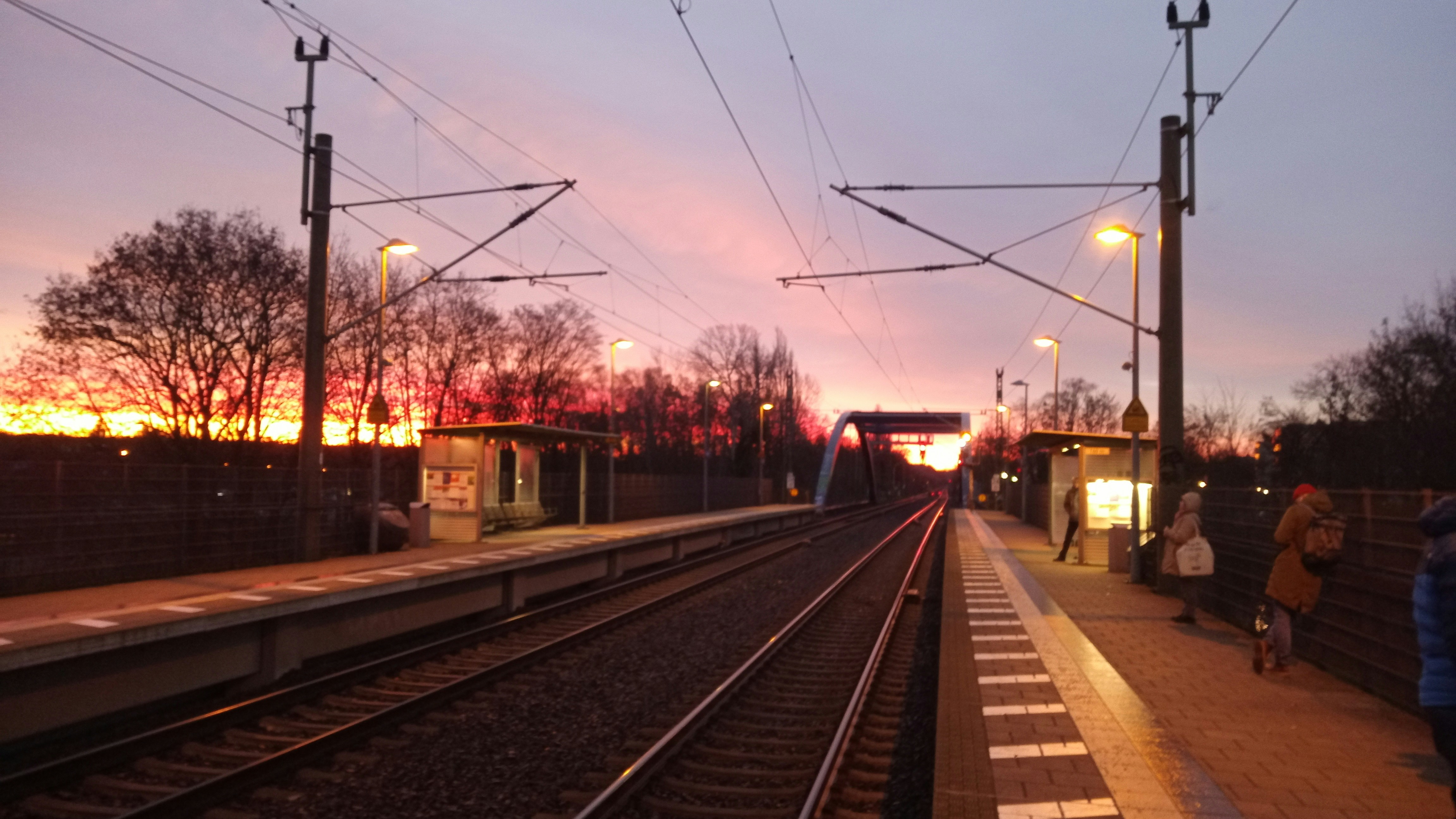 People waiting on a train platform under a vibrant pink and orange sky