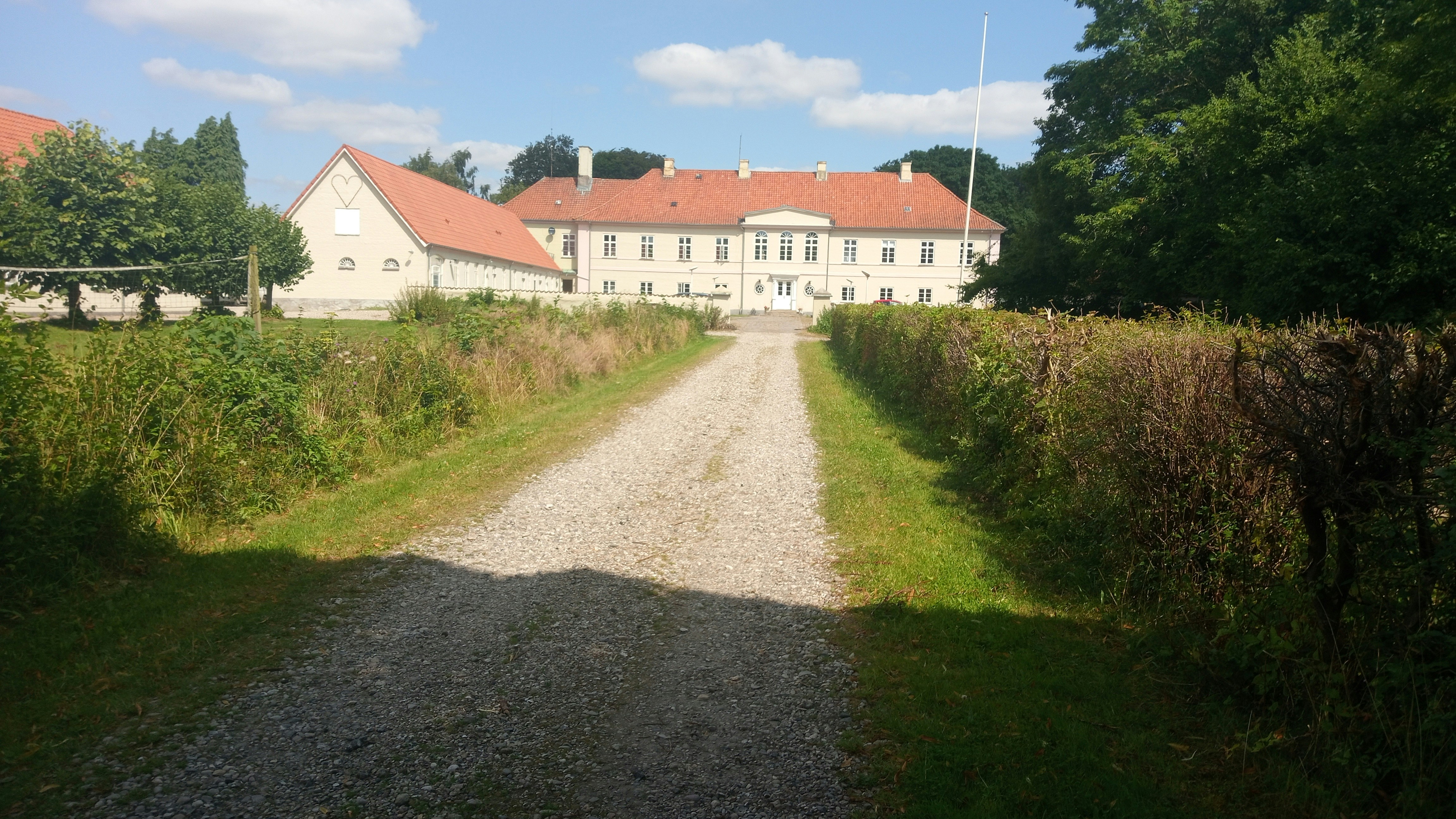 A gravel path leading to a large manor house with a red tiled roof