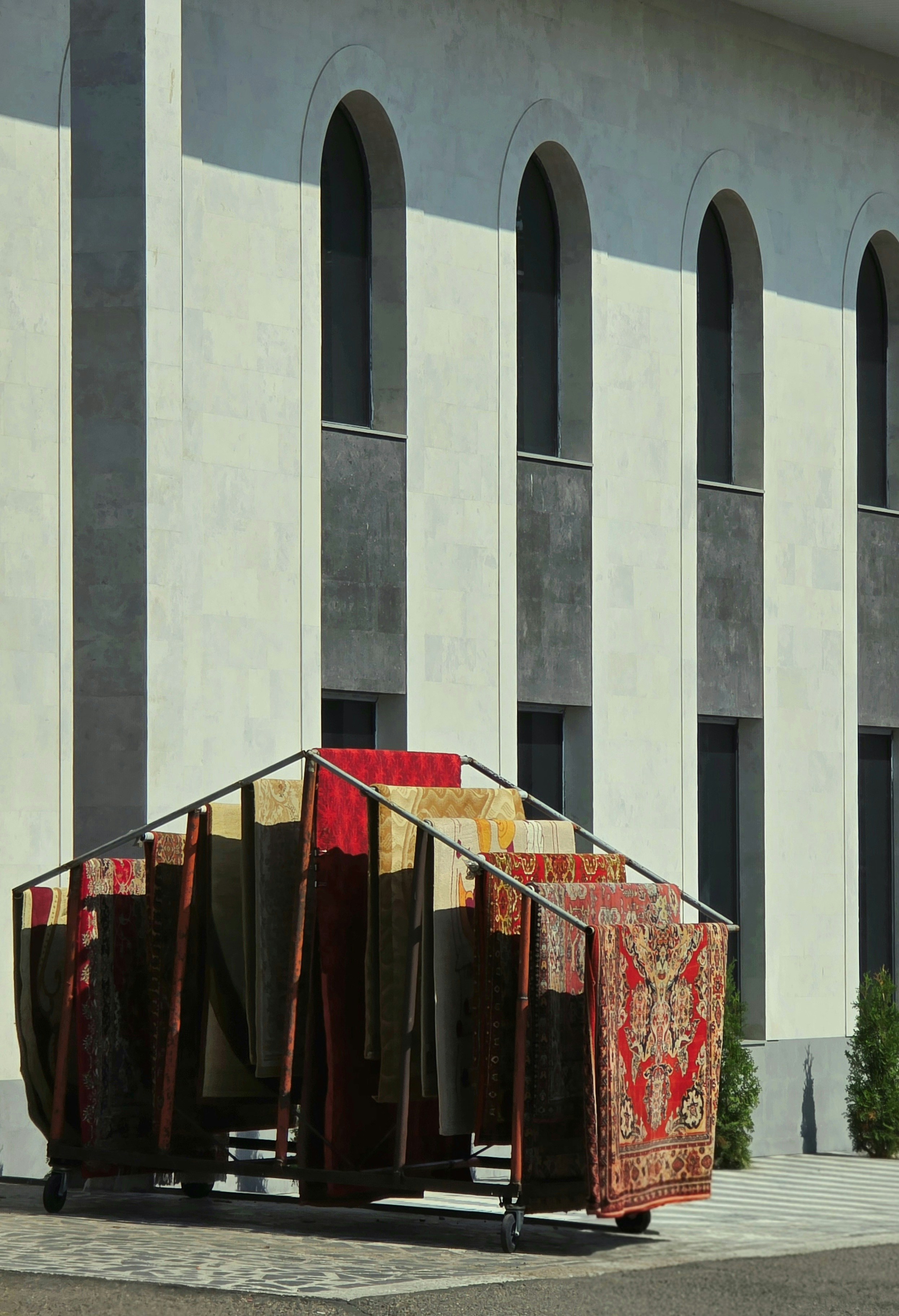 Colorful rug wagon under arched shadows beside a modern facade