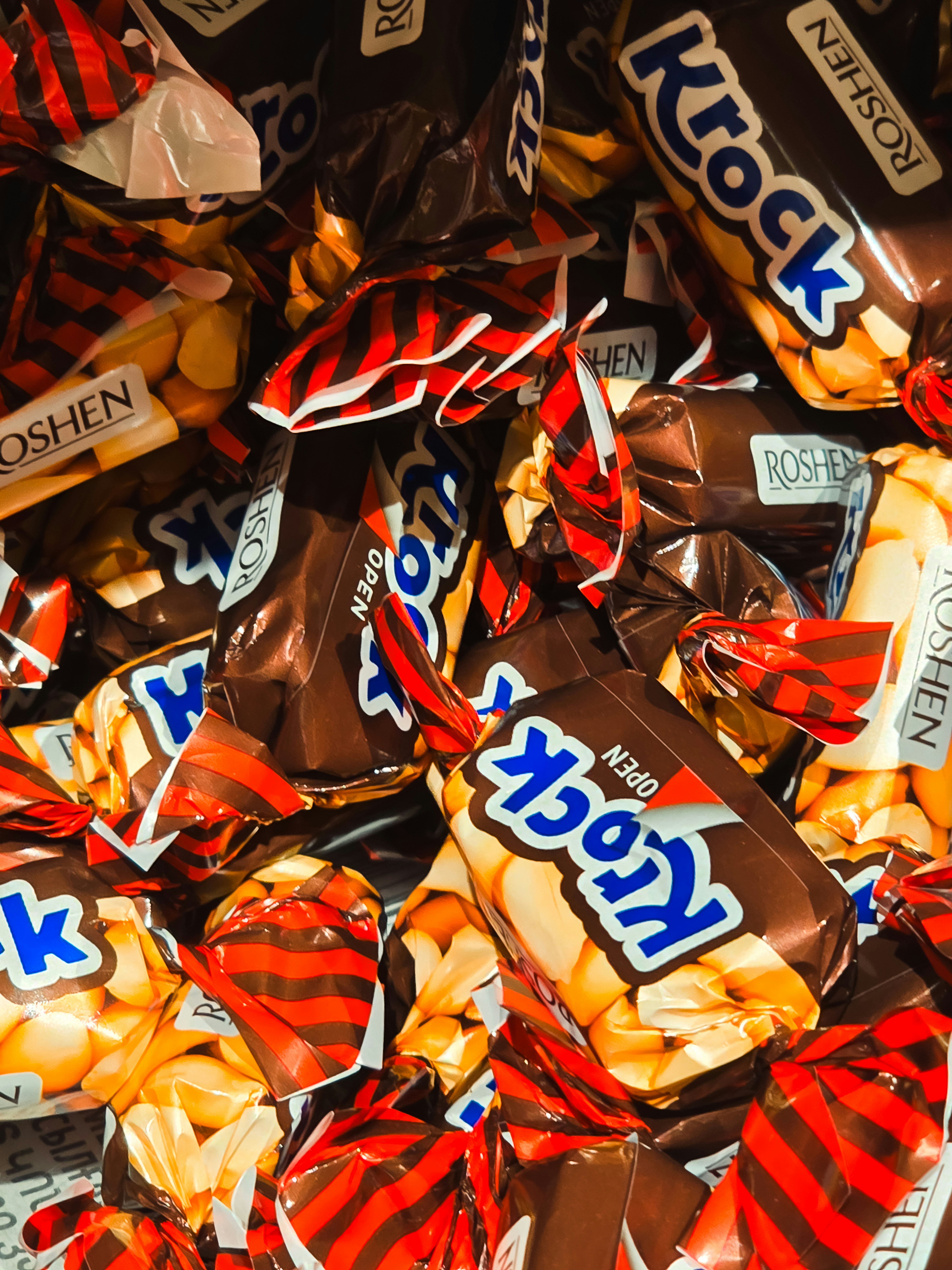 ROSHEN Krock candies, highlighting their individual wrappers and revealing the crunchy caramel confection filled with peanut paste and finished with a cocoa coating.