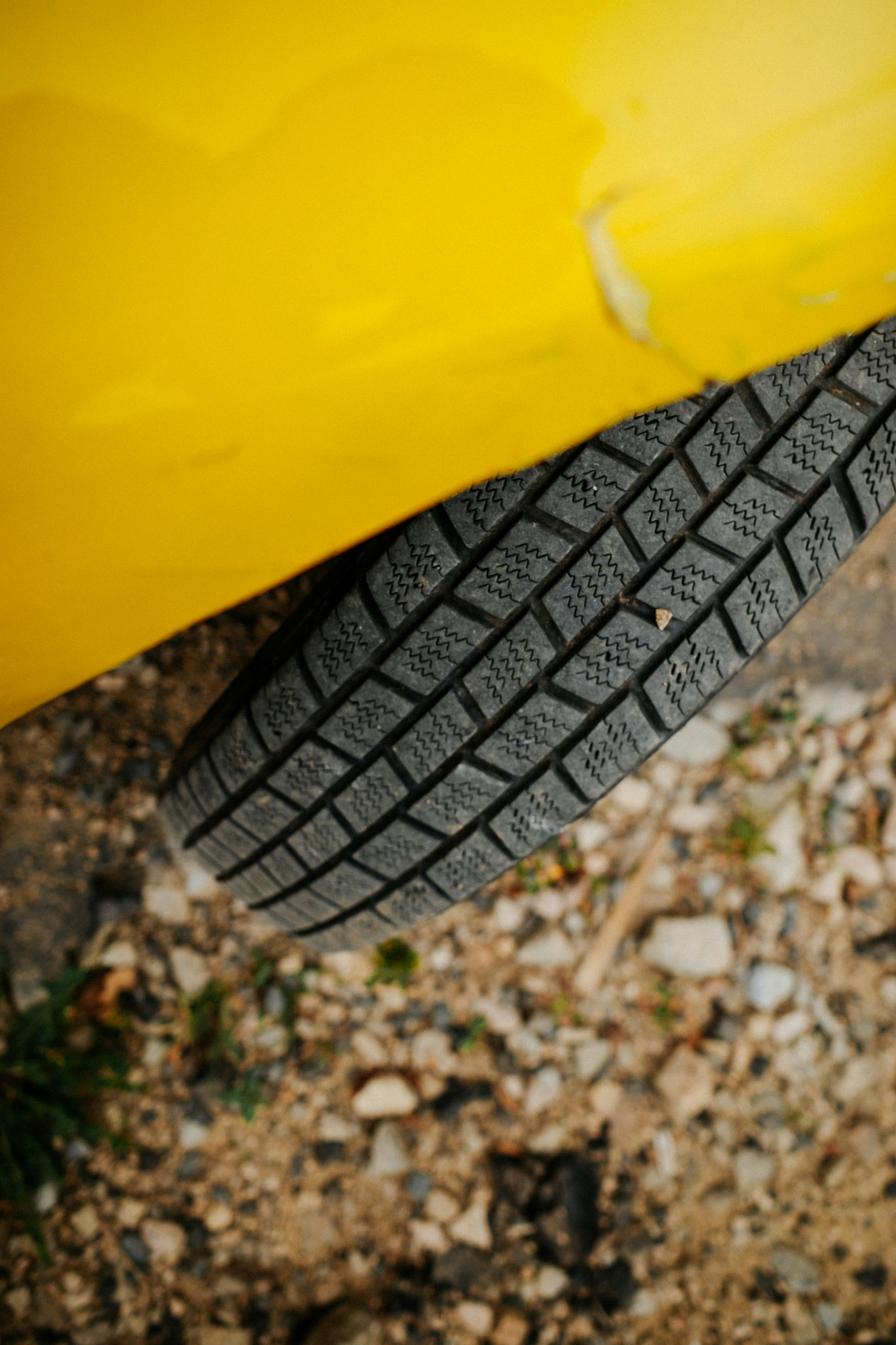 Yellow Car, Worn Tire, and Gravel Ground: A Close-Up of a Vehicle's Side Wheel