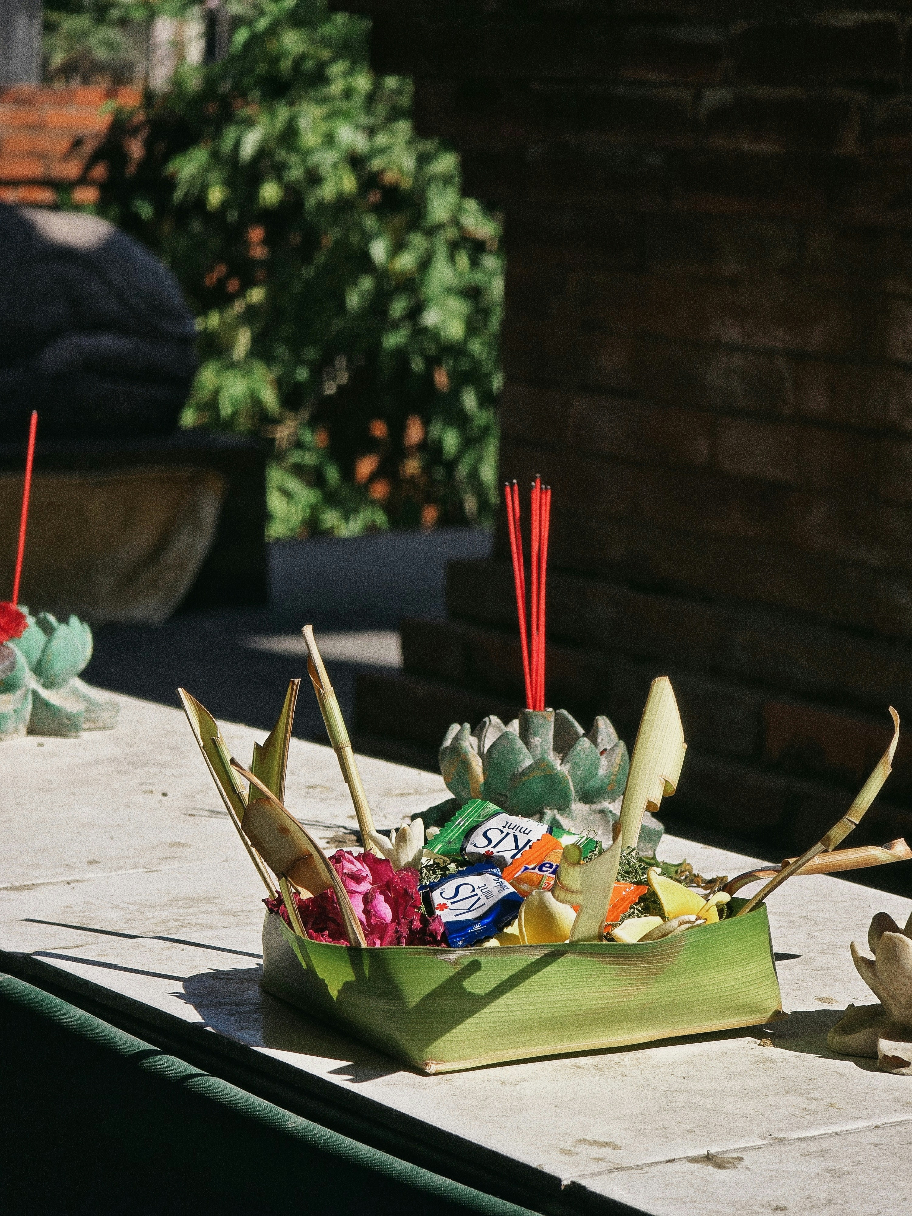 Floating offering: a vibrant banana leaf basket with incense sticks on sunlit stone