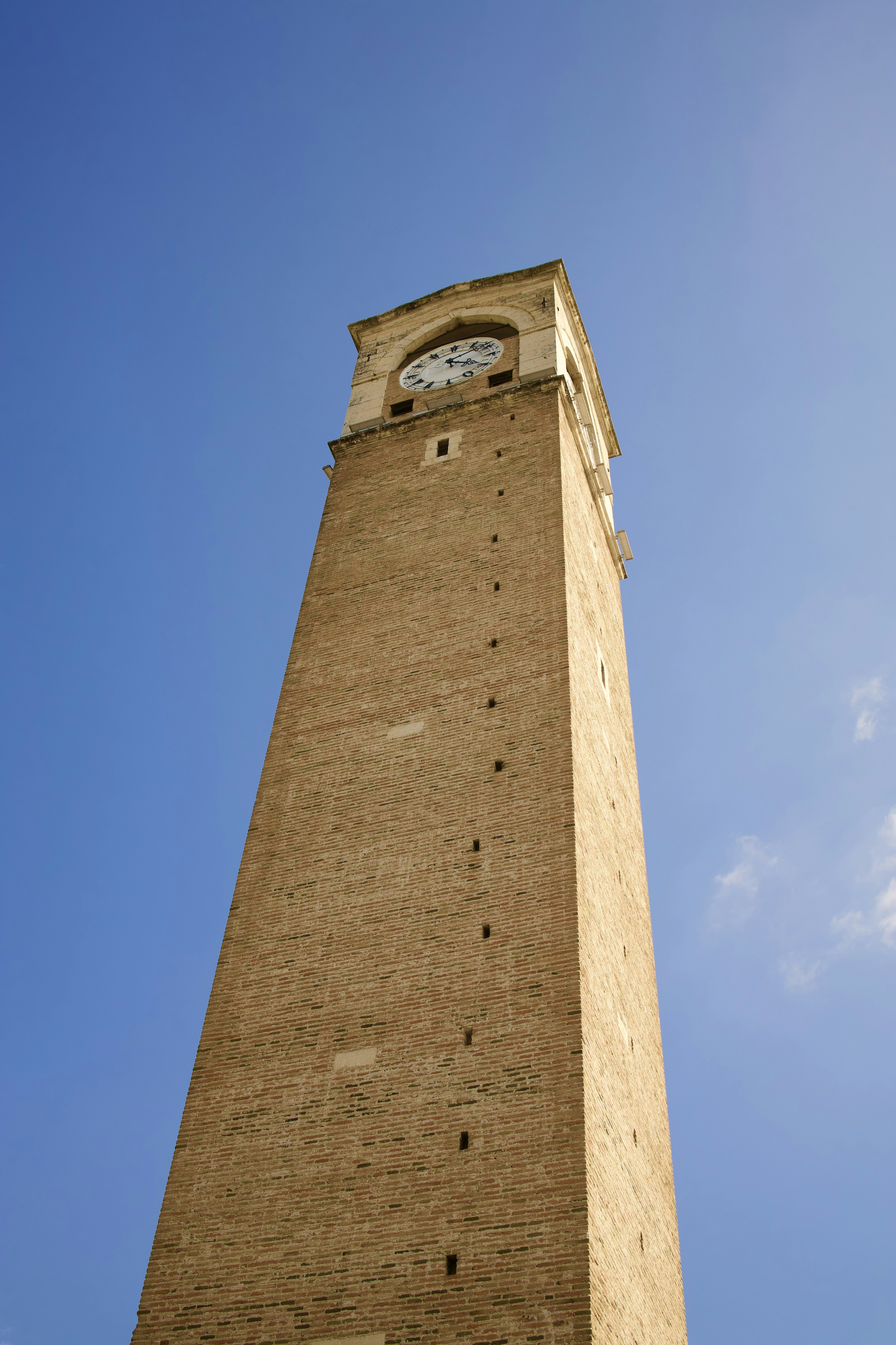 Tall brick clocktower rising against a clear blue sky with a visible clock face near the top; minimal surrounding context emphasizes the structure.