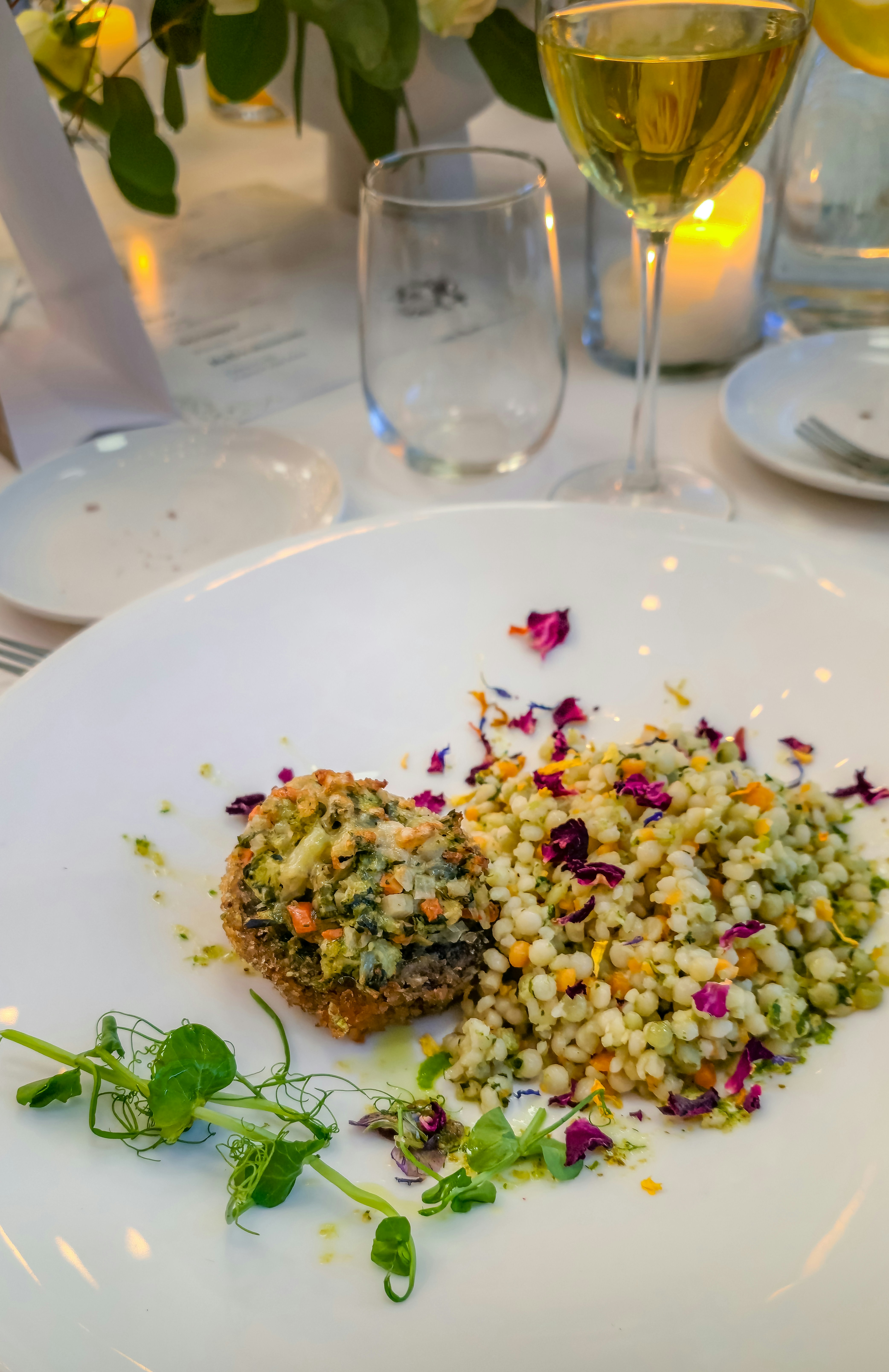 Herbed Croquette and Pearl Couscous plated with floral garnish at a candlelit table