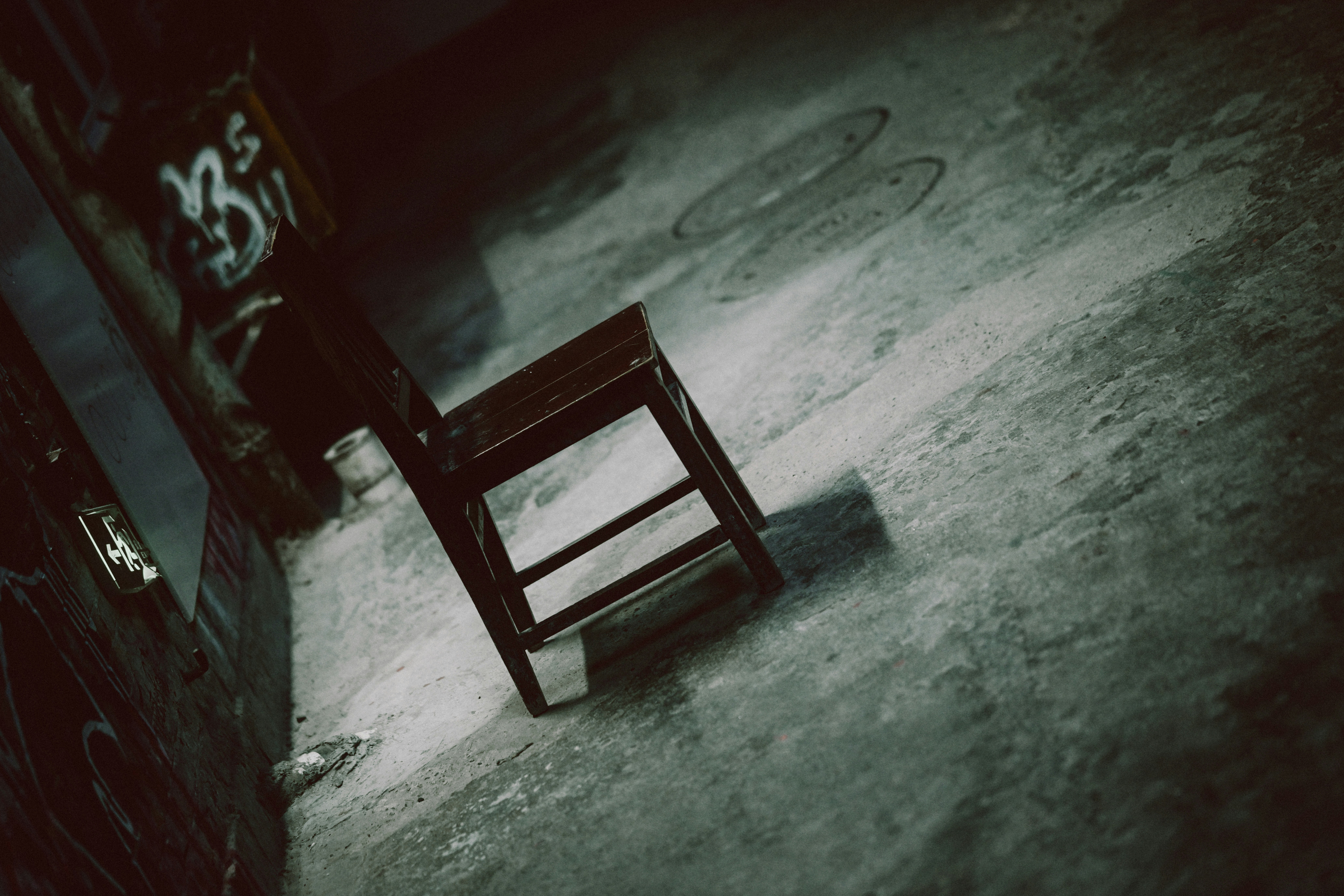 A dark wooden chair on a concrete surface beside a graffiti covered wall