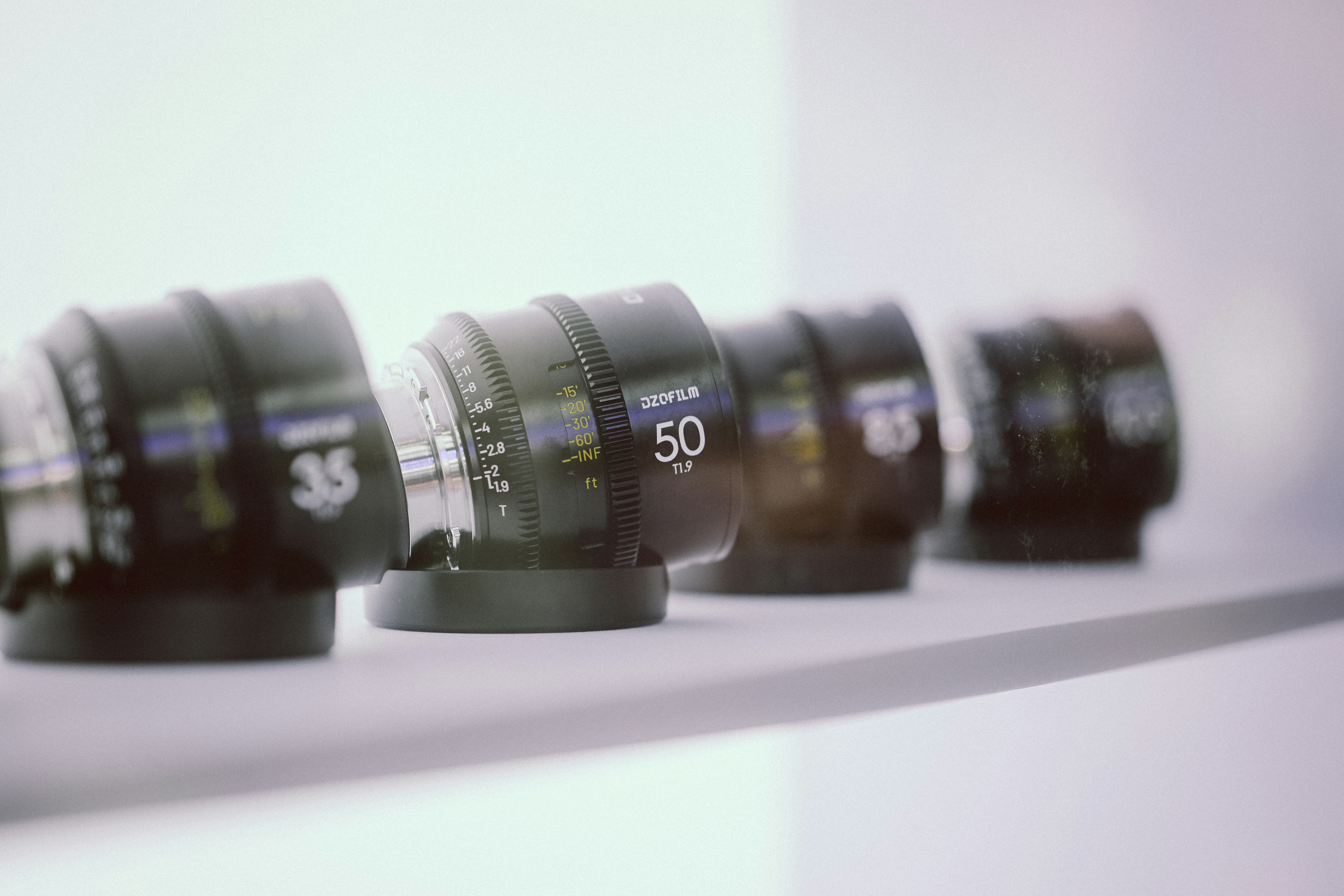 A row of vintage cinema lenses on a white shelf, softly blurred