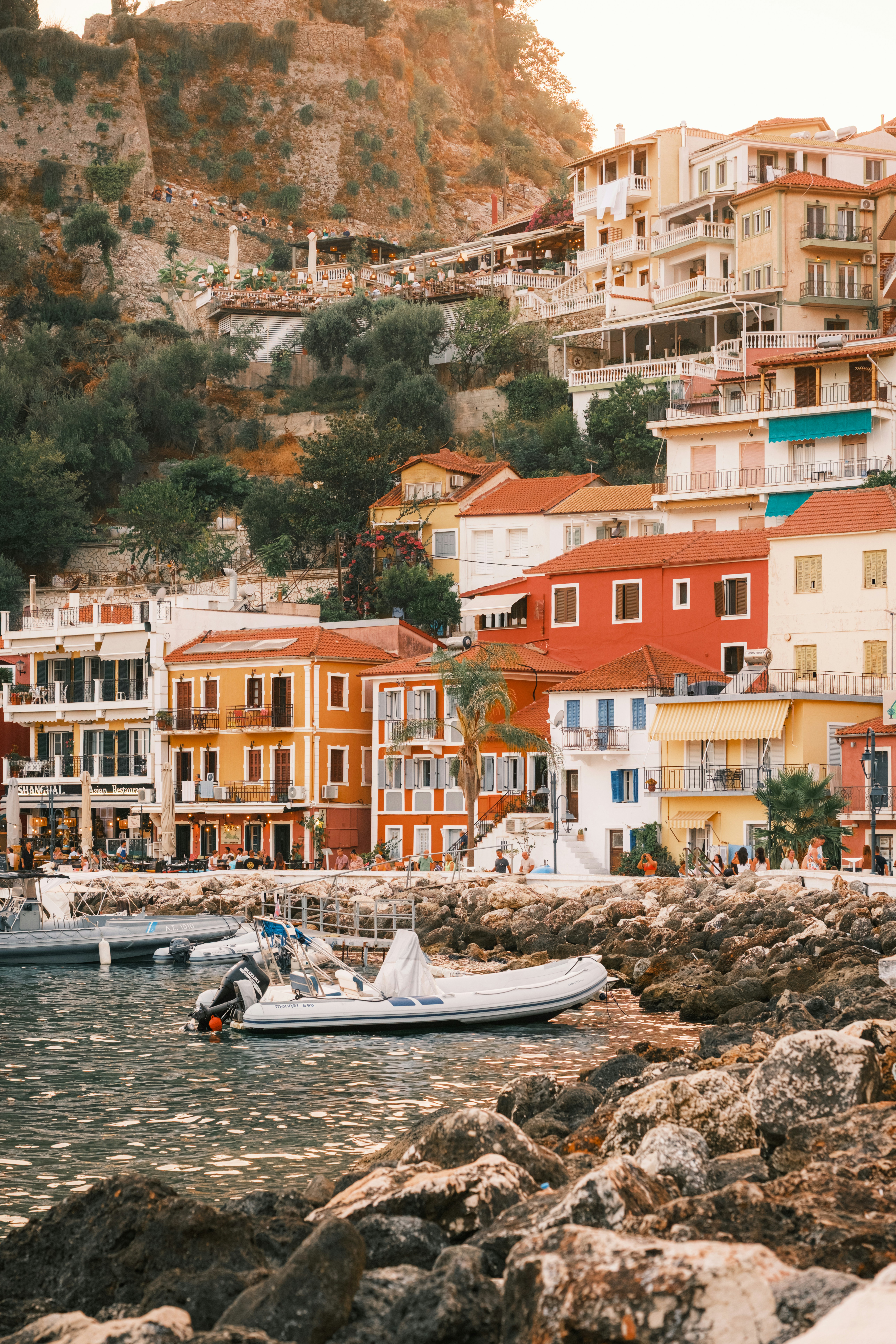 Quaint Mediterranean coastal town with vibrant buildings stacked along the hillside and boats resting in calm harbor water.
