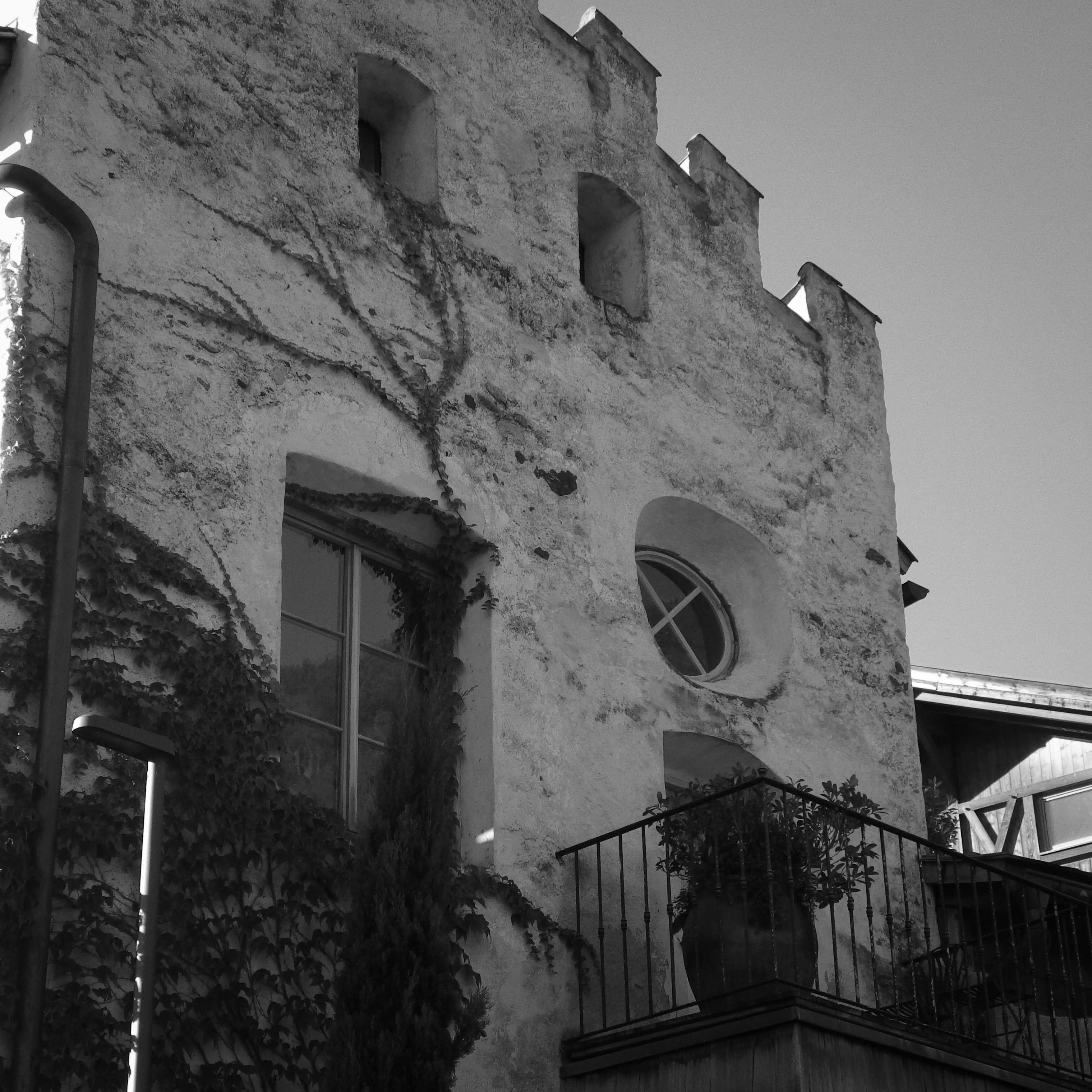 Ivy-clad stucco building with a round window and balcony, captured in grayscale to emphasize texture and architectural detail.