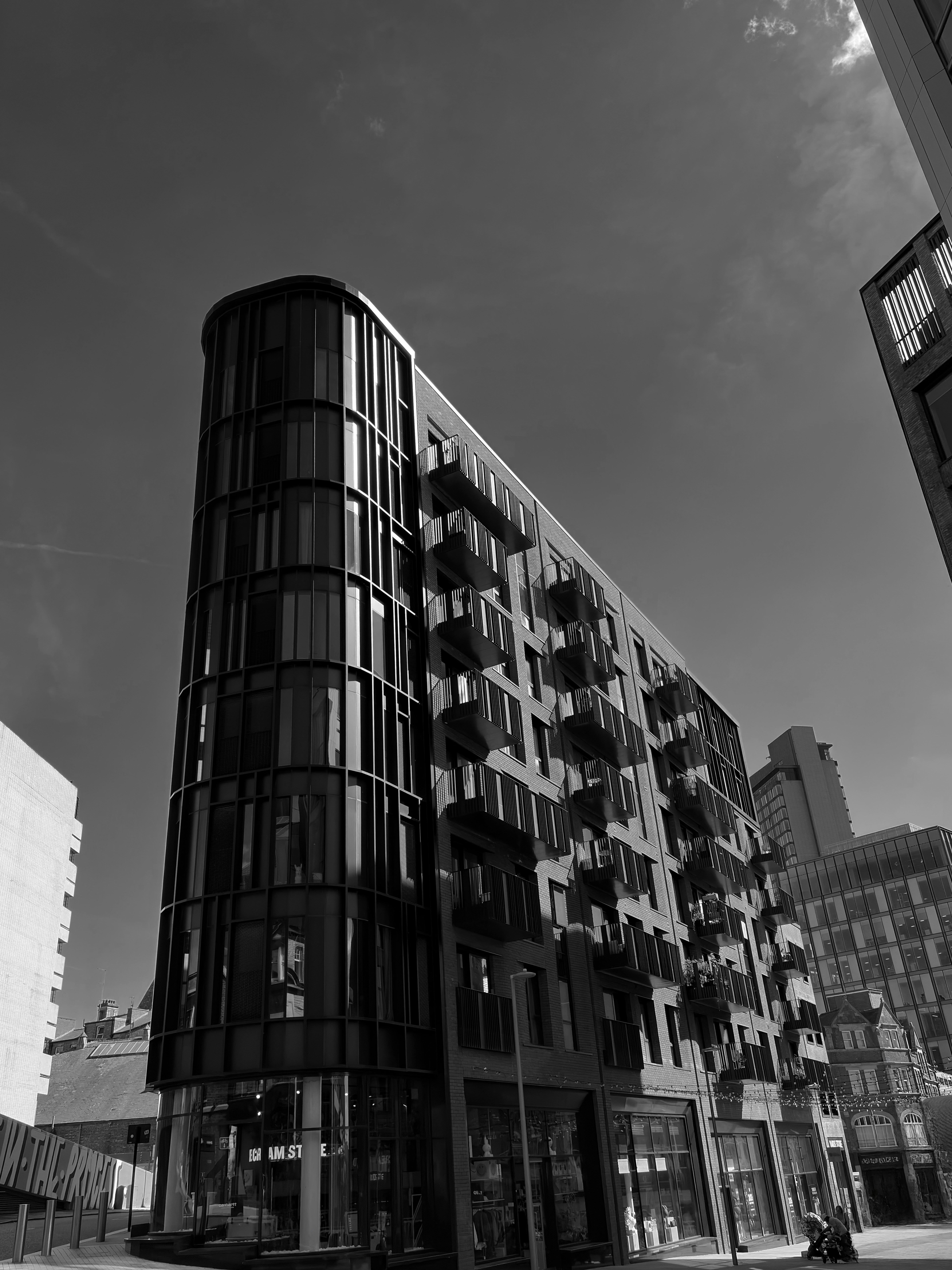 Sleek multi-story building with rounded glass tower on a city street, captured in black and white to emphasize structure and shadows.