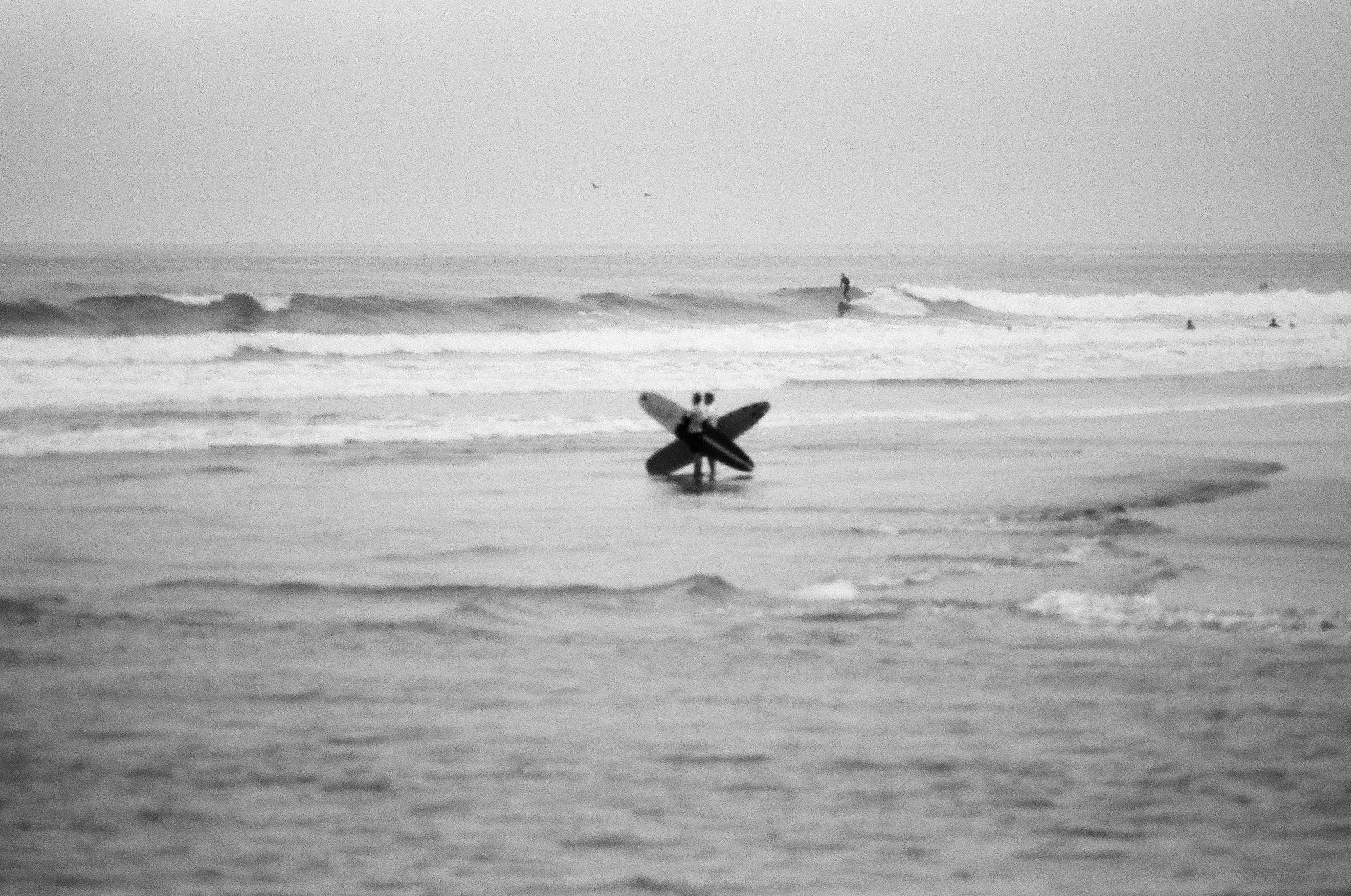 Surfboard silhouettes and distant surfer drift across a quiet shoreline
