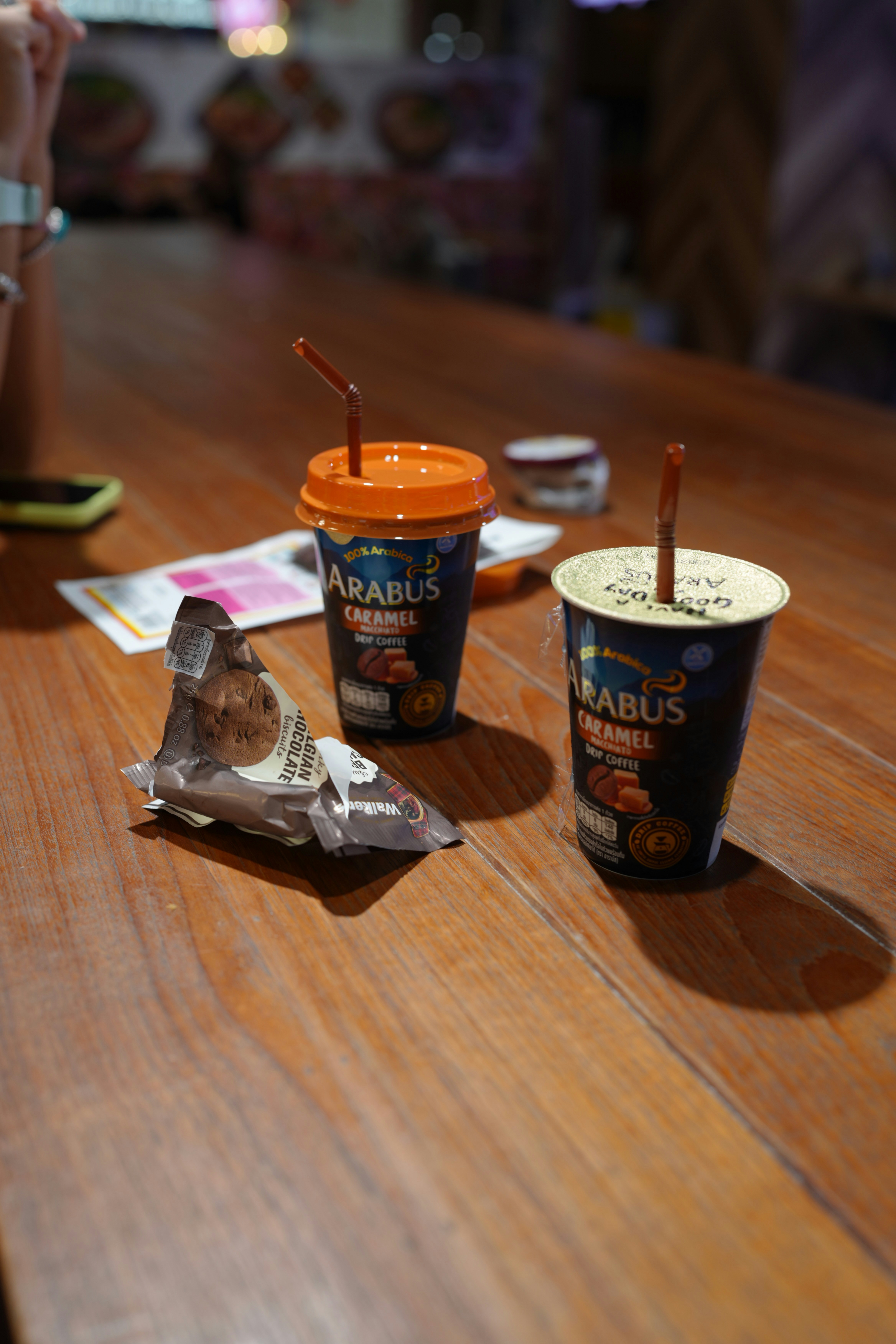 Two Caramel Cups on a Wooden Table with a Crumpled Snack Pack