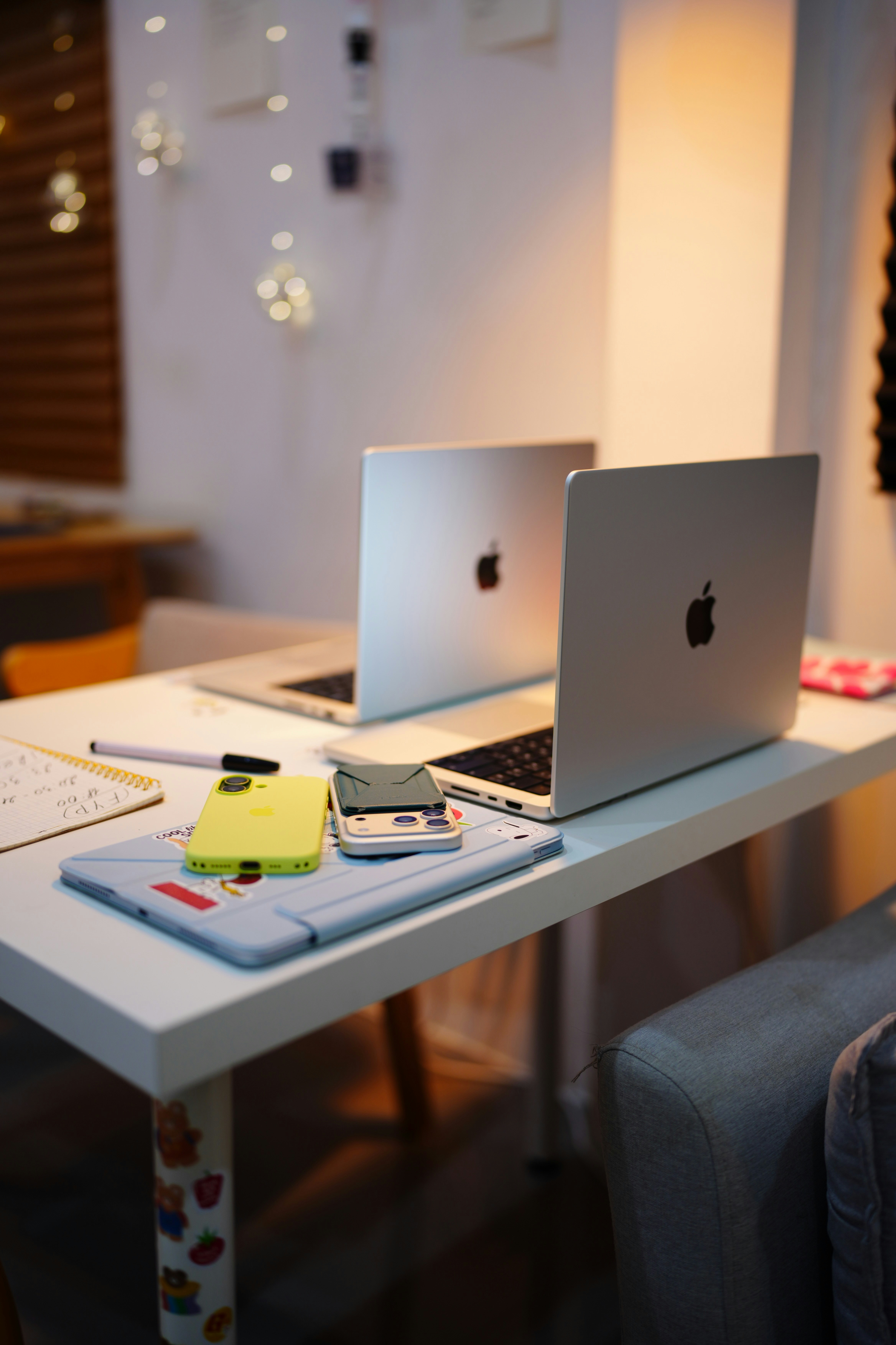 Worktable Echo: Silver MacBooks and a Neon Green Phone Unite Under Warm Desk Light