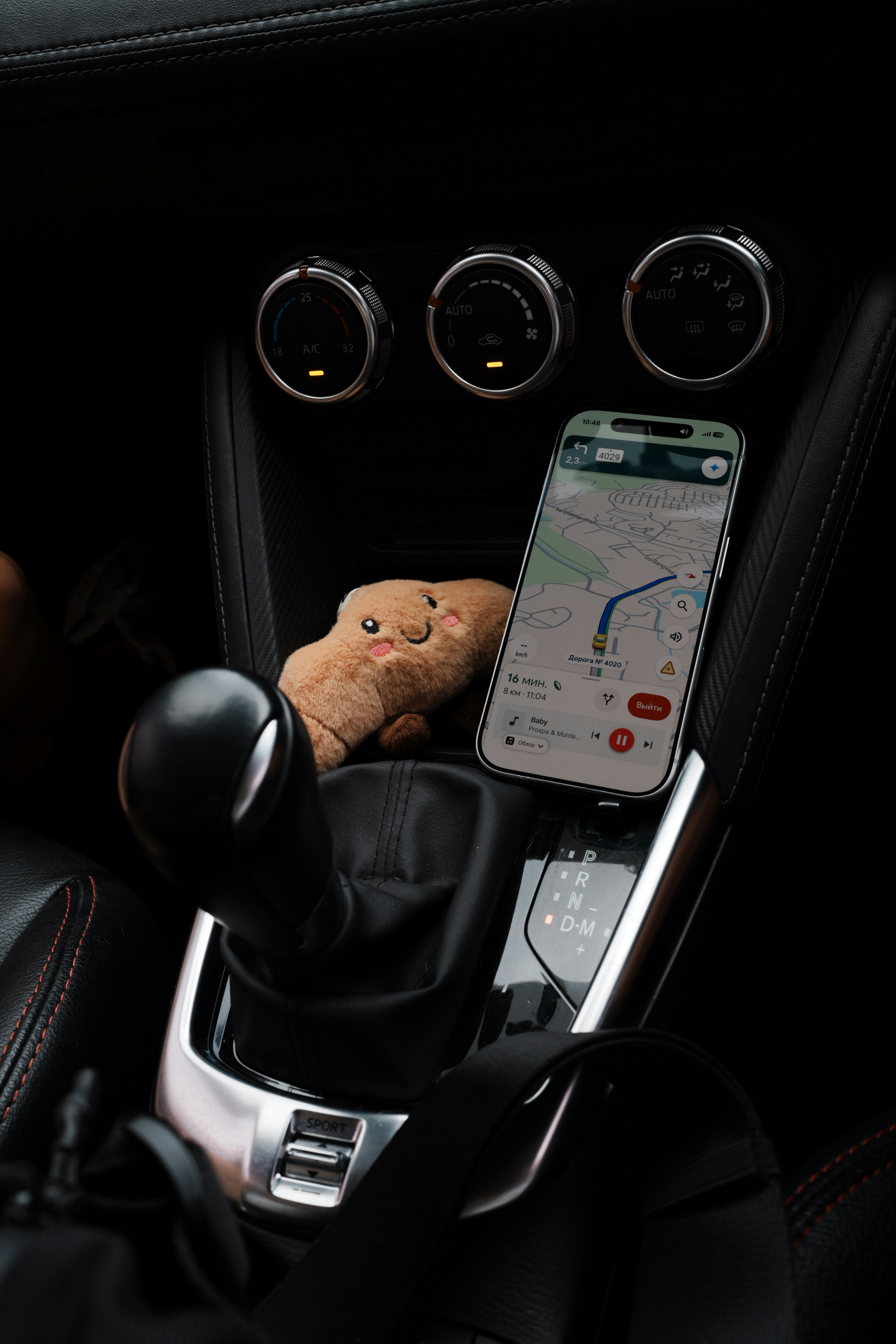 An iPhone displaying a GPS navigation app resting in a car center console next to a small plush bunny toy.