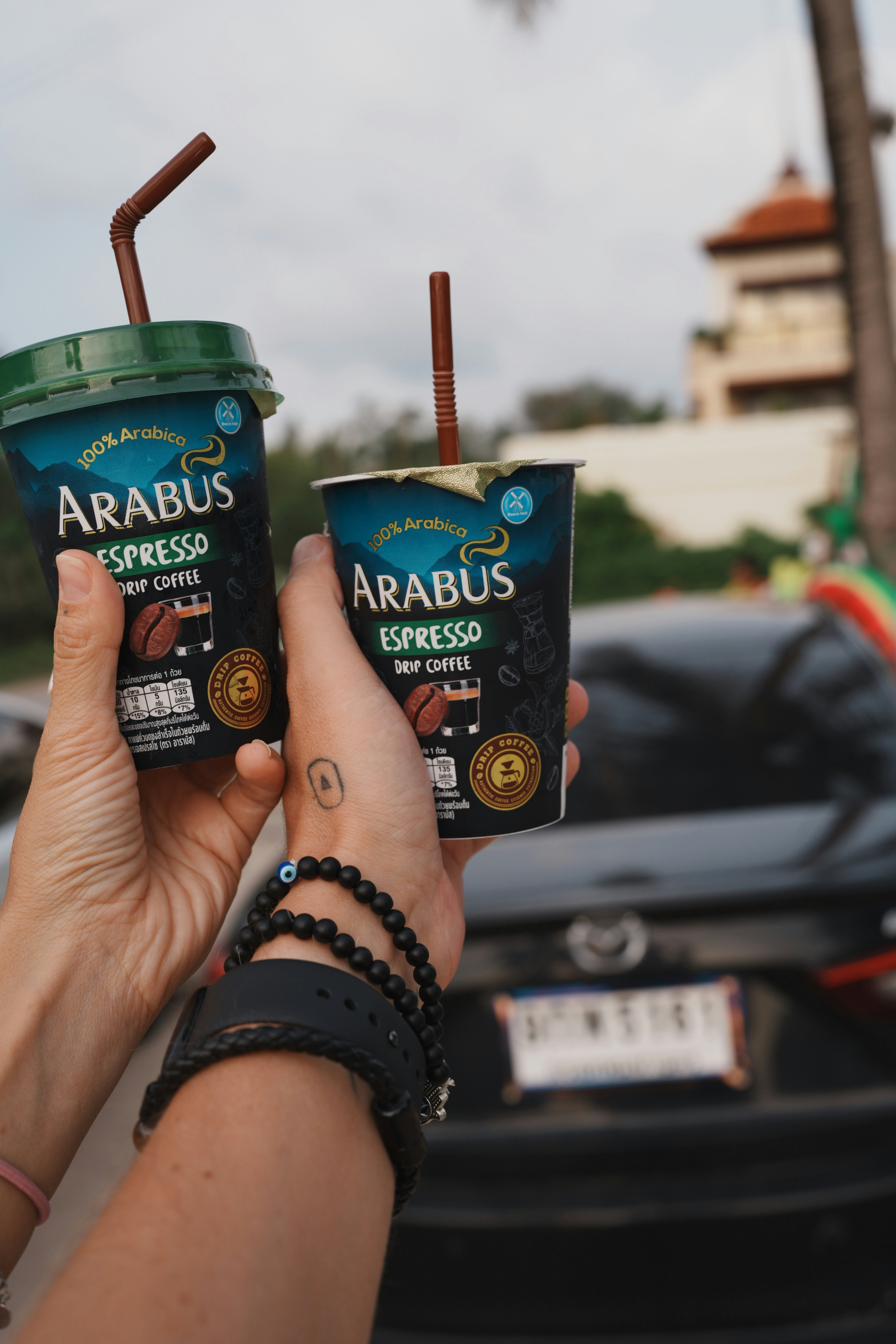 Two Arábus Espresso Cups Raised Against a Blurred Street Scene