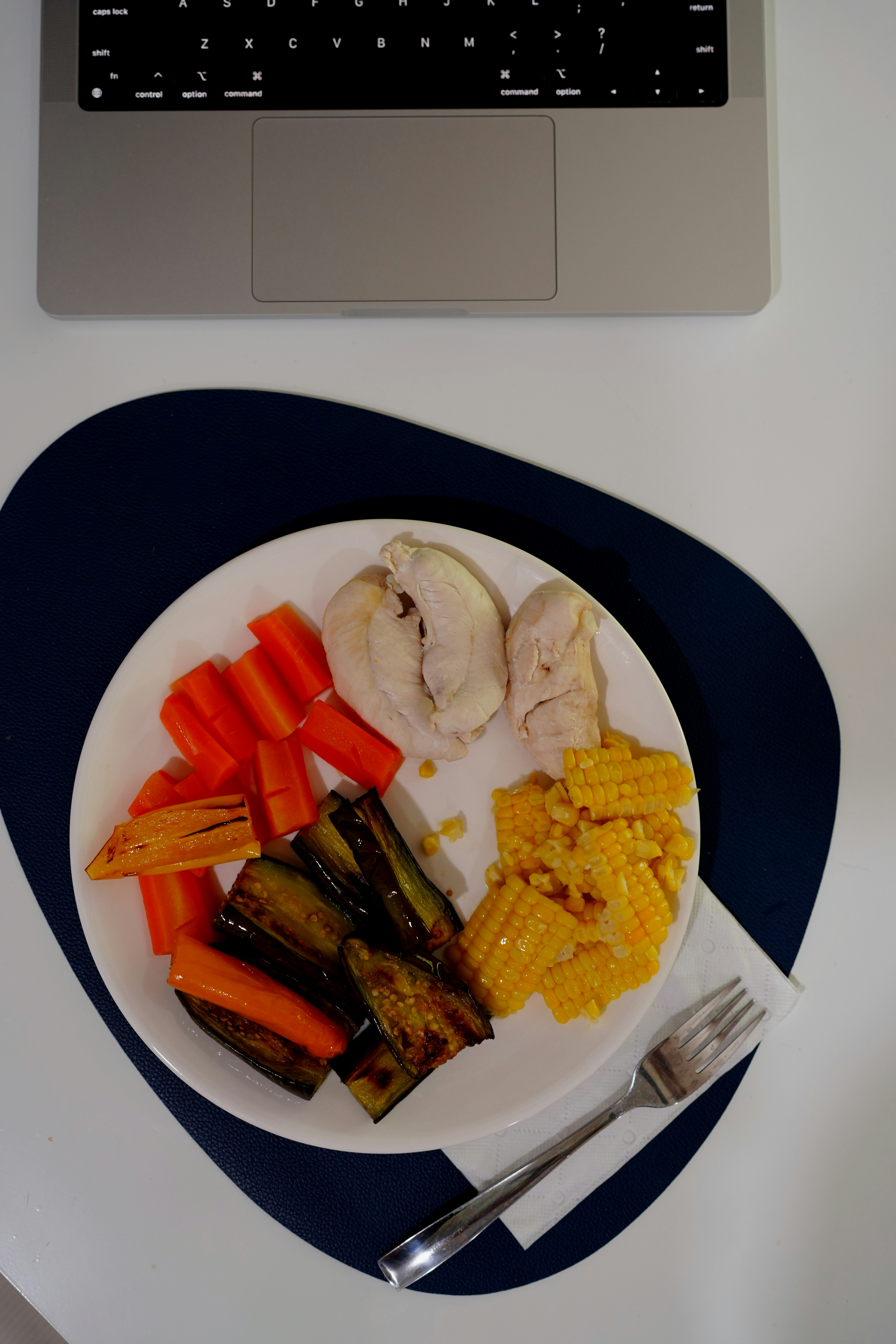 Overhead plate: colorful vegetables and corn with chicken pieces on a dark placemat