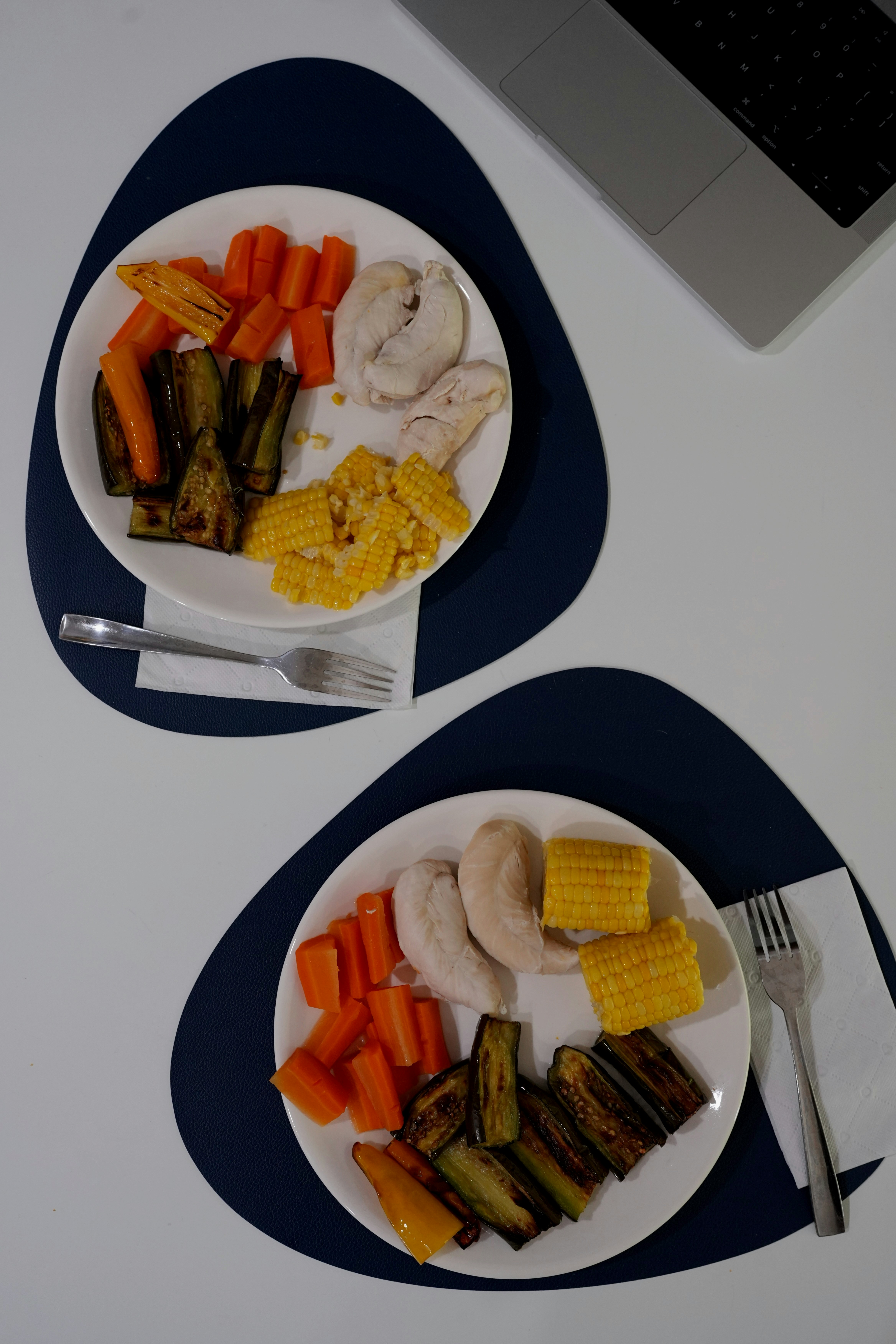 Two plate settings for a casual veggie feast beside a laptop