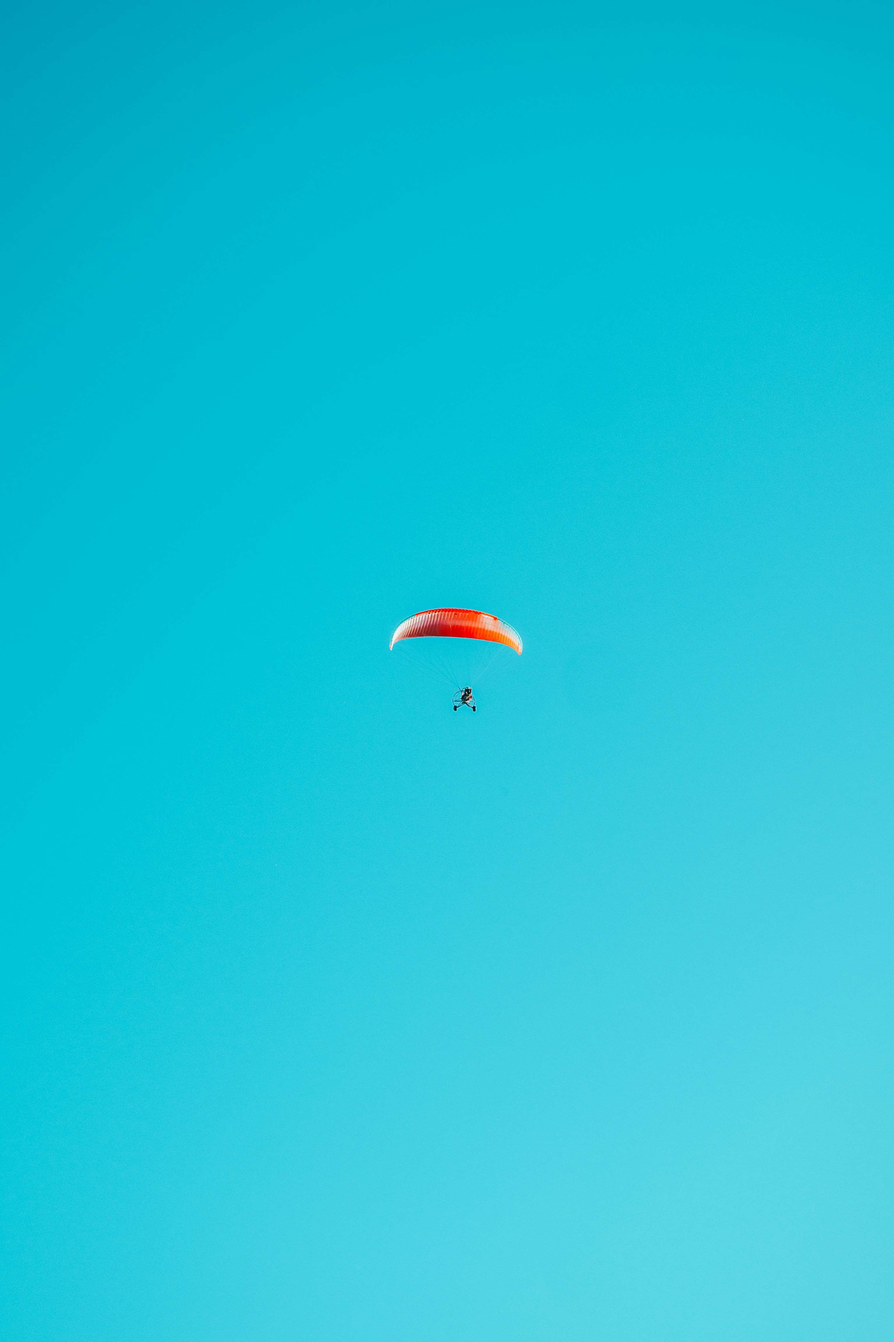 Daring Descent: Paraglider Silhouetted in a Cyan Sky