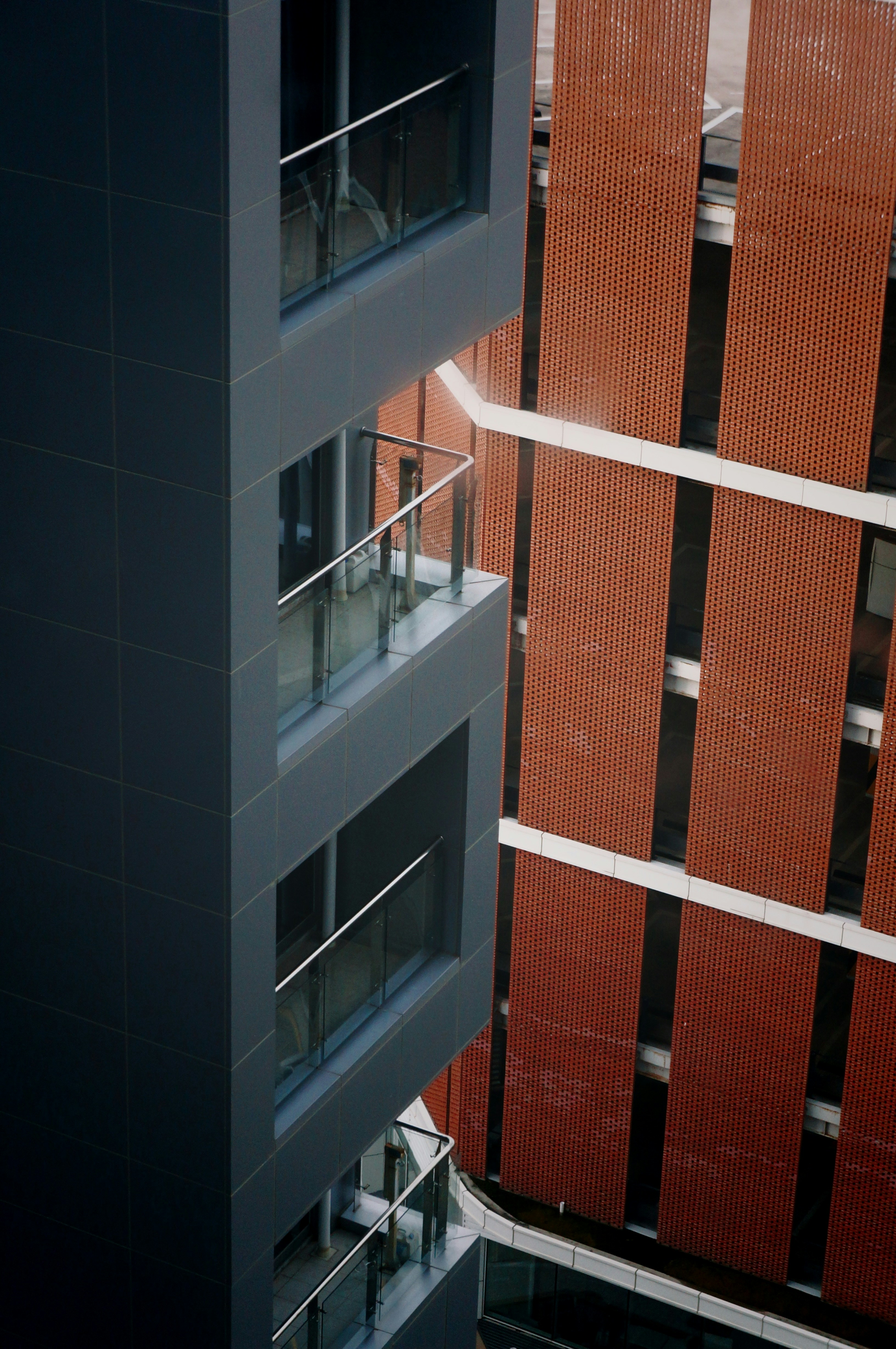 Modern architectural forms collide in a diagonal frame of blue-gray concrete and orange brick panels, creating a rhythmic interplay of lines and shadows.