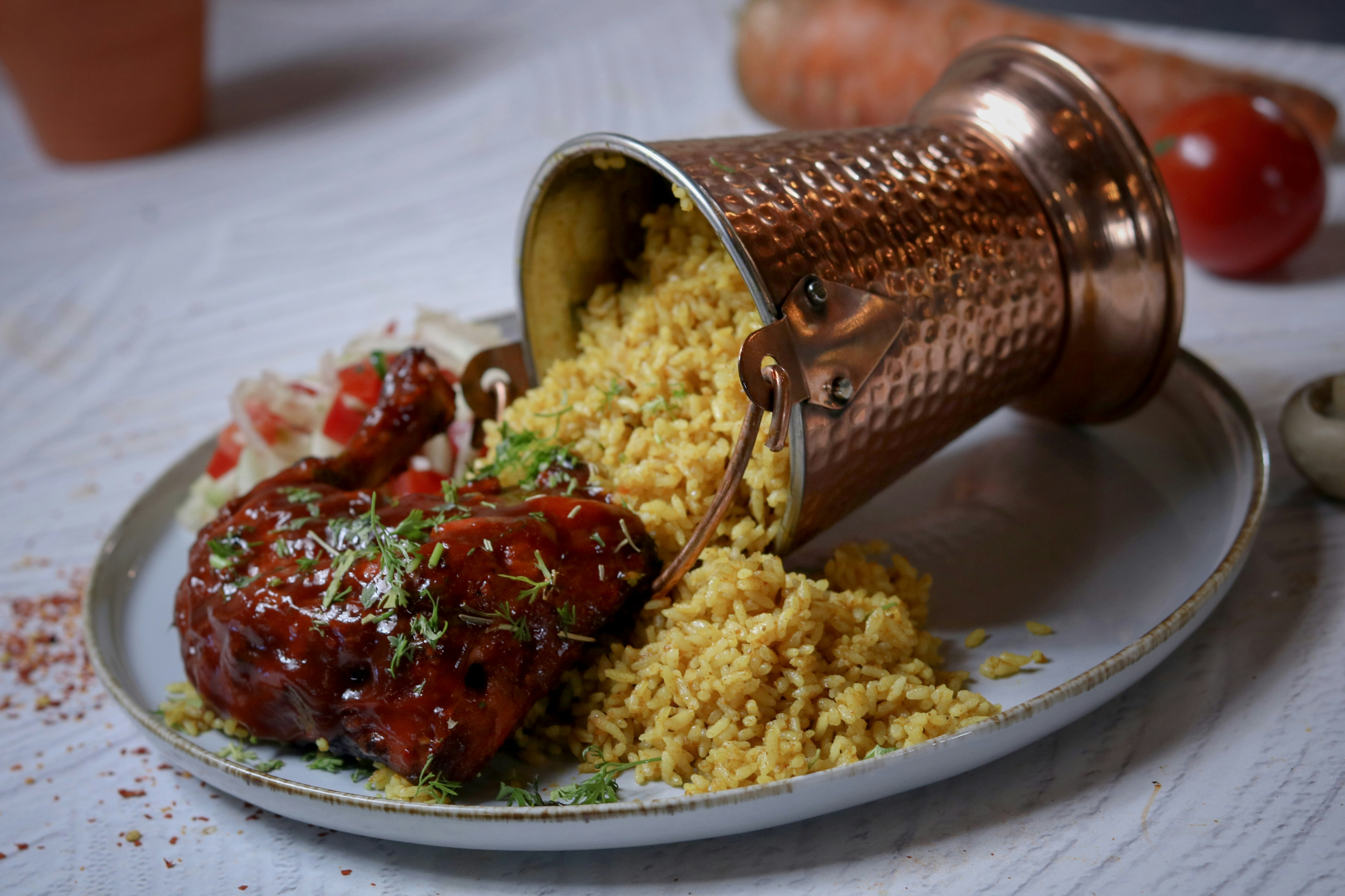Copper-grained pepper mill pours golden couscous beside glazed meat on a plate