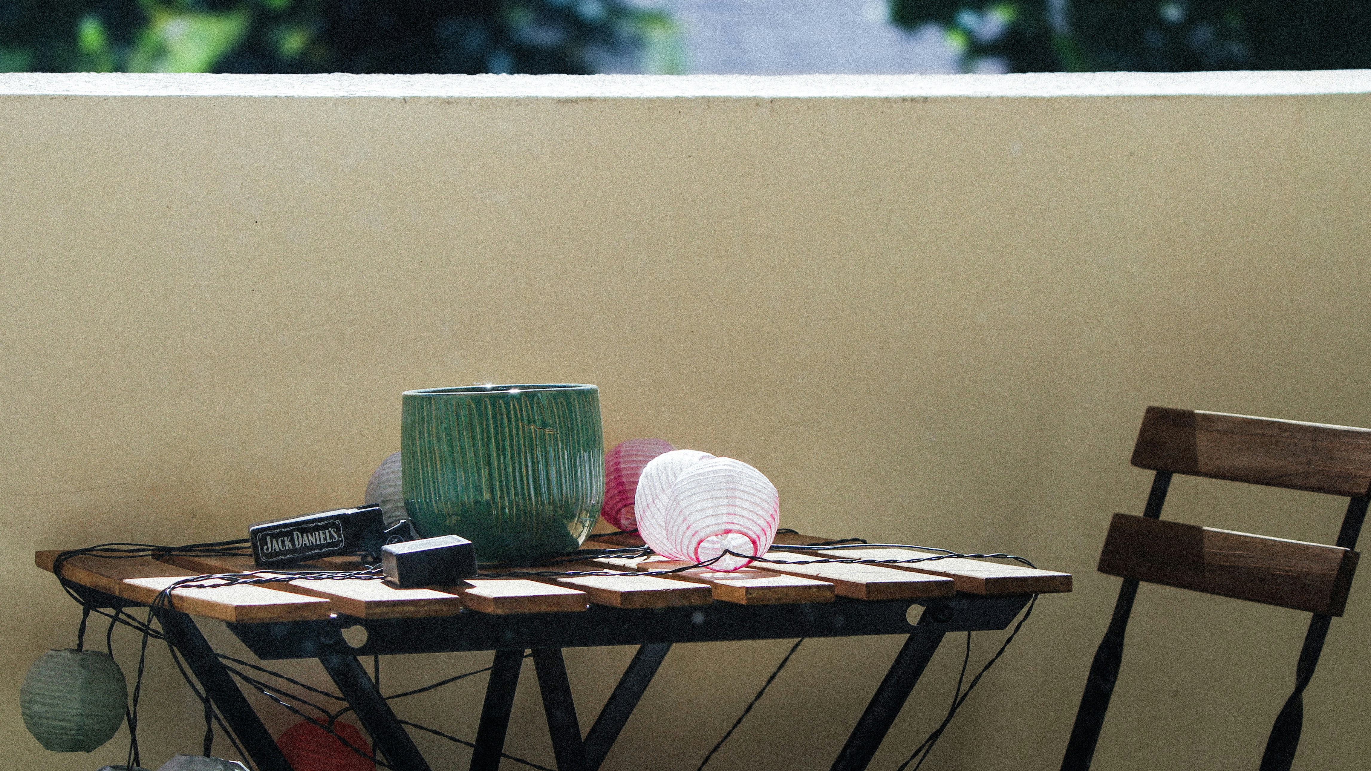 Sunlit outdoor table with decorative lanterns and a few small objects on a tiled surface; a wooden chair sits nearby on a balcony. This is a typical still-life scene with soft natural light.