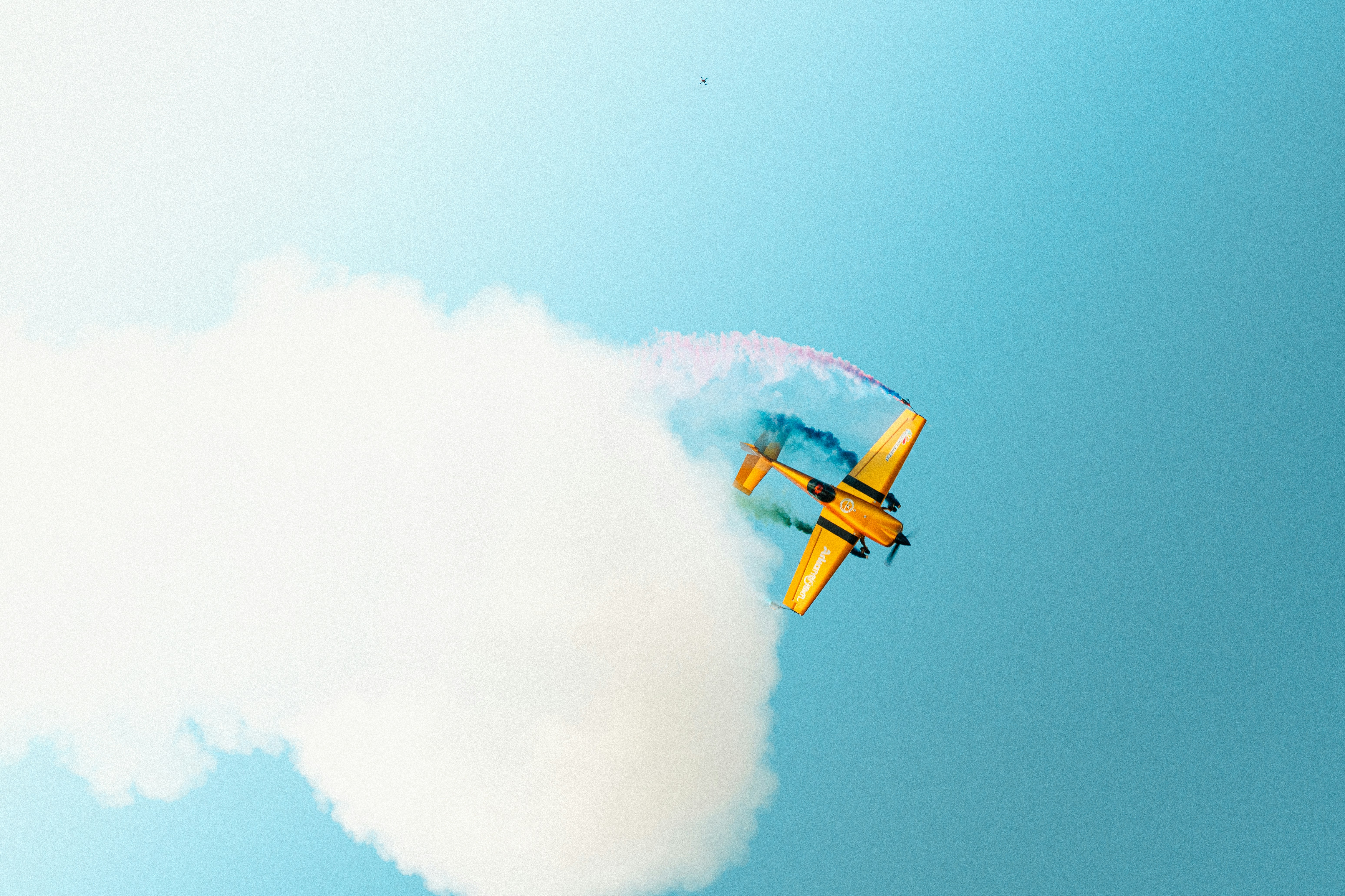 Bright yellow biplane leaving a plume of white smoke against a vivid blue sky.