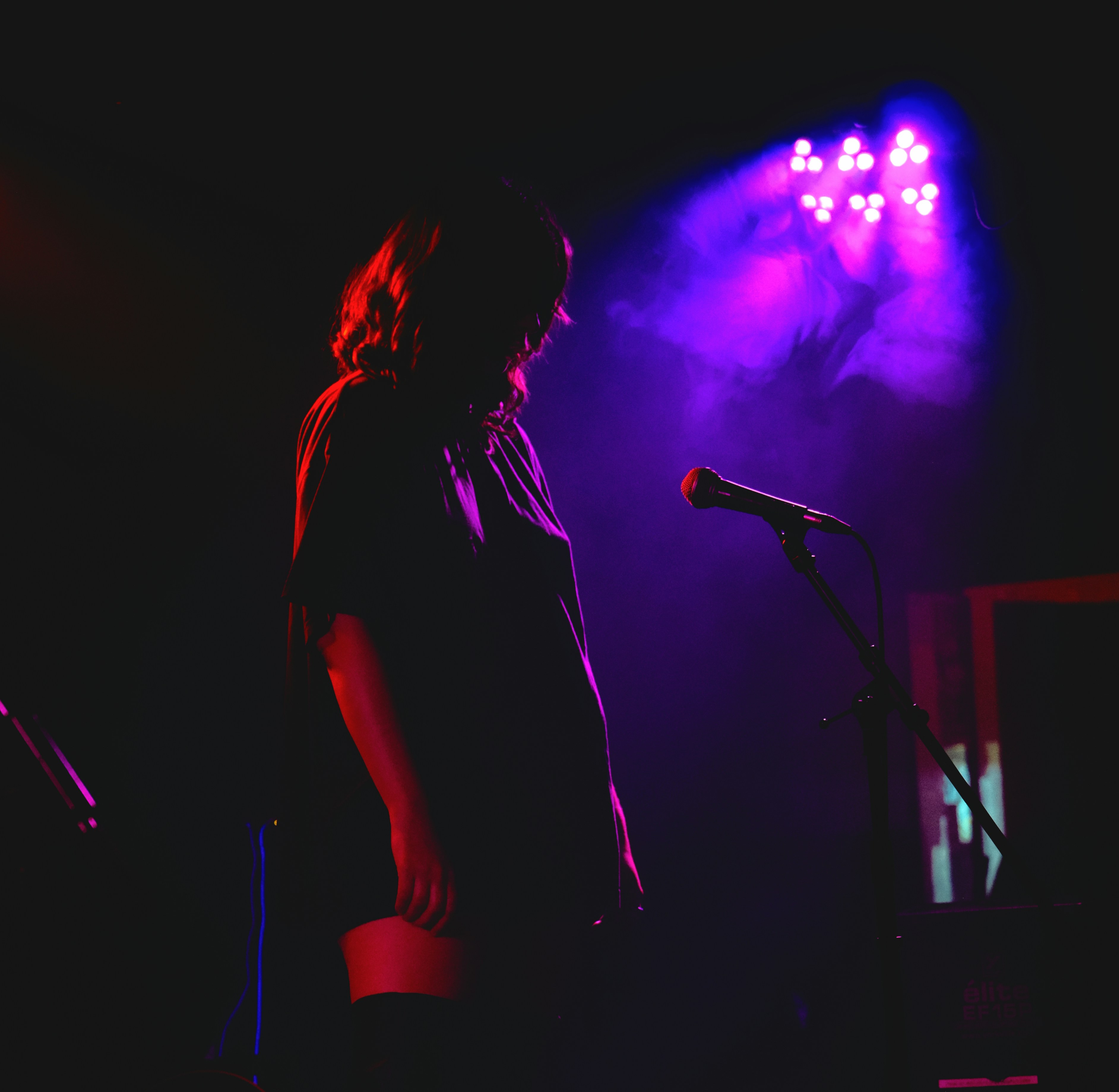 Silhouette at the Microphone: Neon Haze Over a Quiet Stage