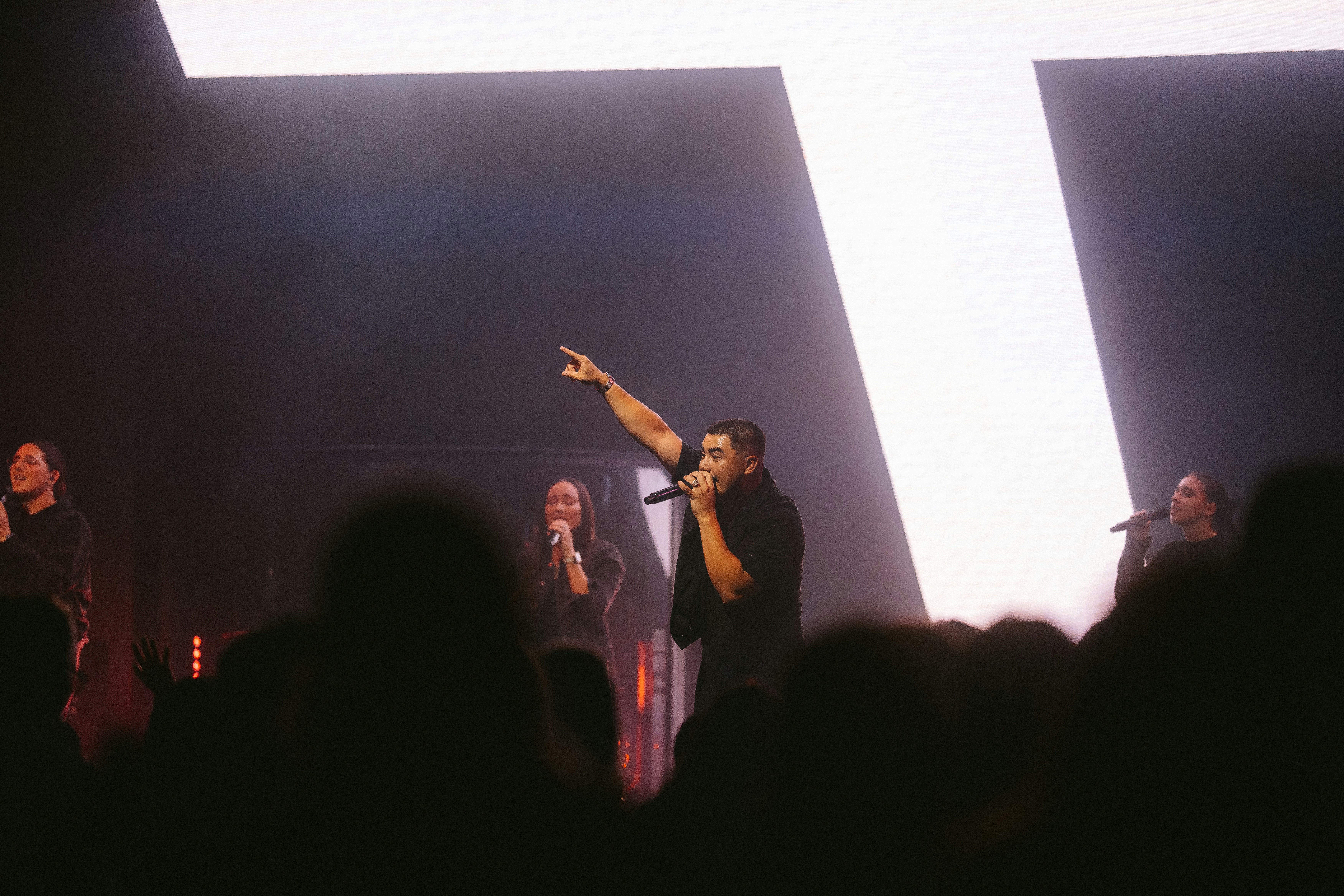 Midstage Spotlight: A Vocalist Leads with Raised Arm under a Backlit Cross