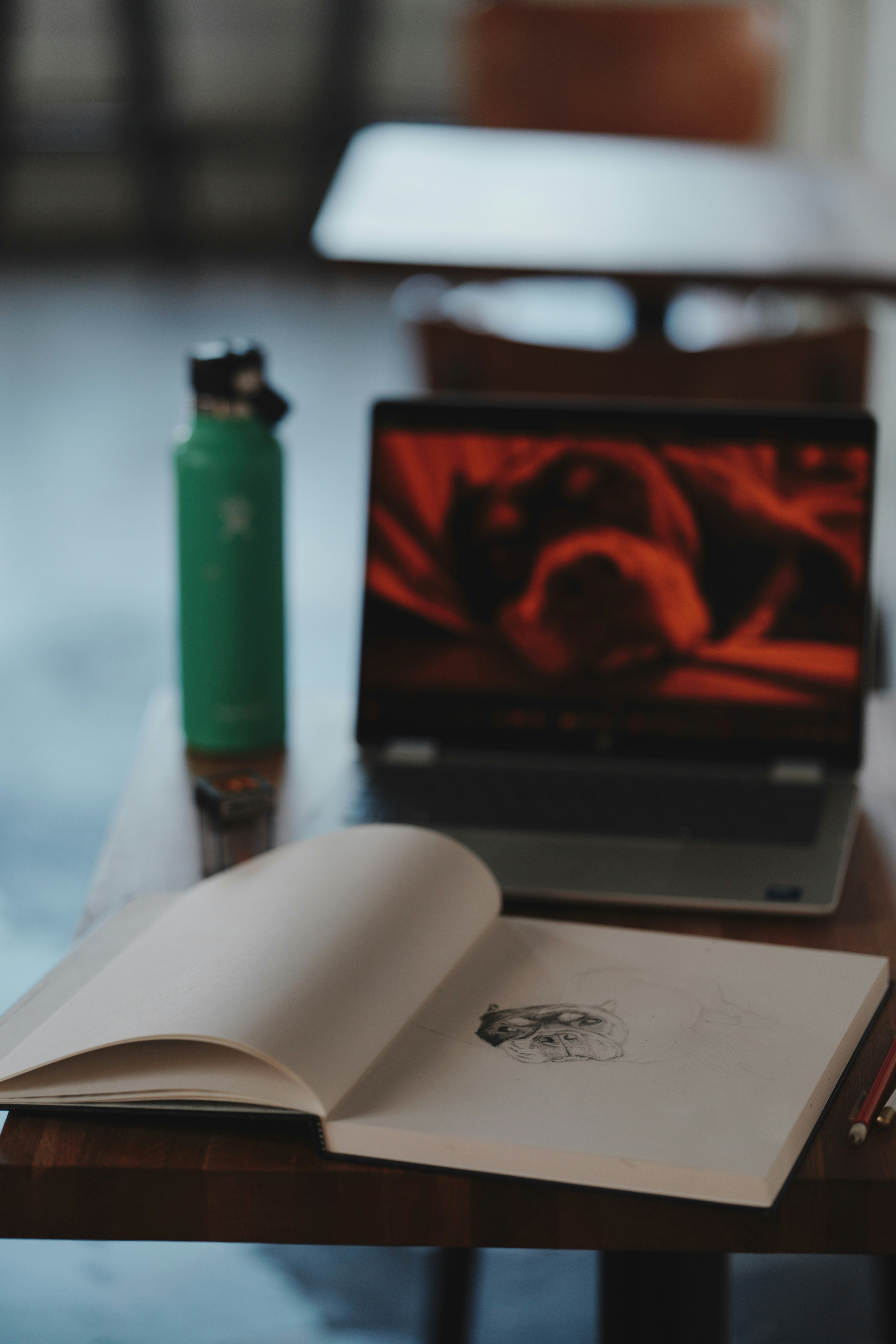 Desk-side Sketches: A Laptop, Sketchbook, and Green Bottle in Soft Focus