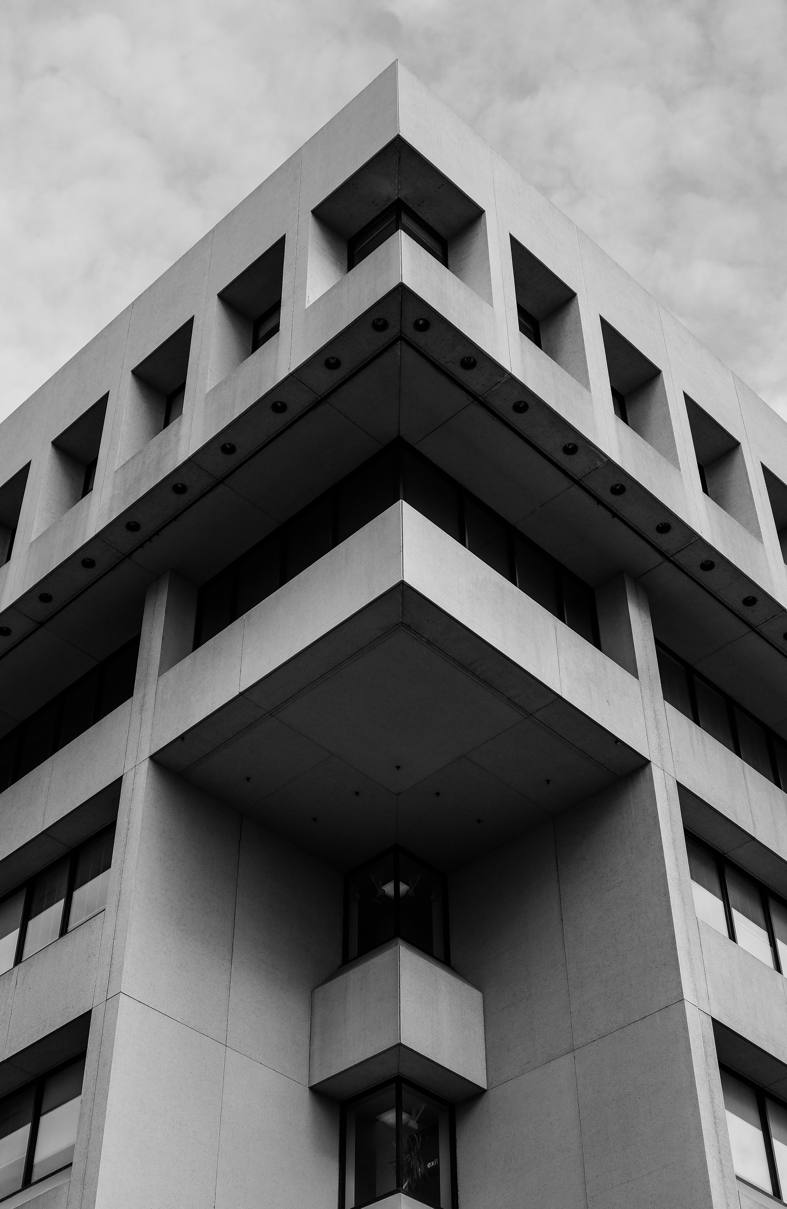 Monochrome architectural facade with strong diagonal lines creating a layered corner perspective, emphasizing modular windows and protruding balcony elements.