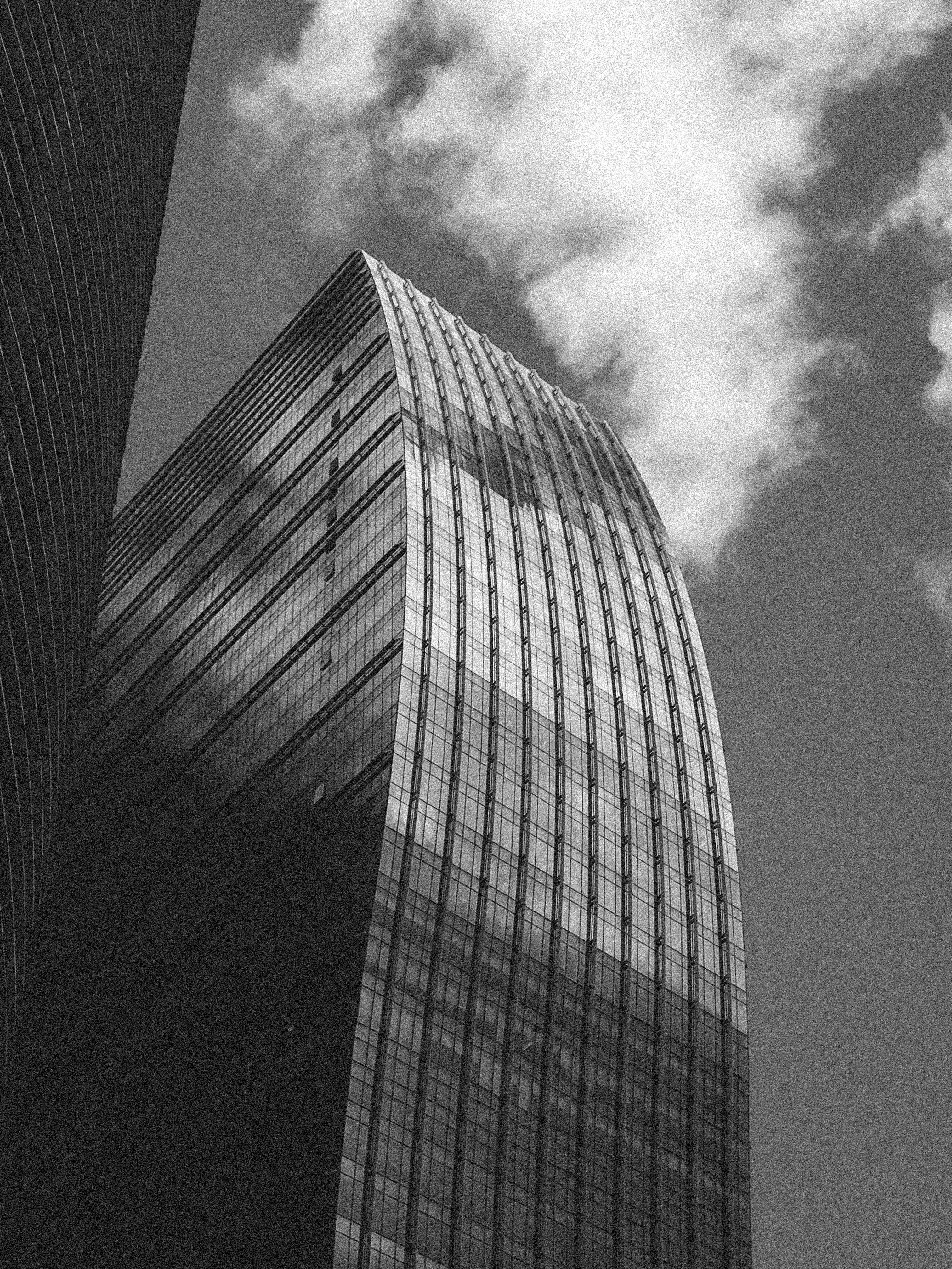 Sleek glass skyscraper ascends beside a darker structure under a partly cloudy sky.