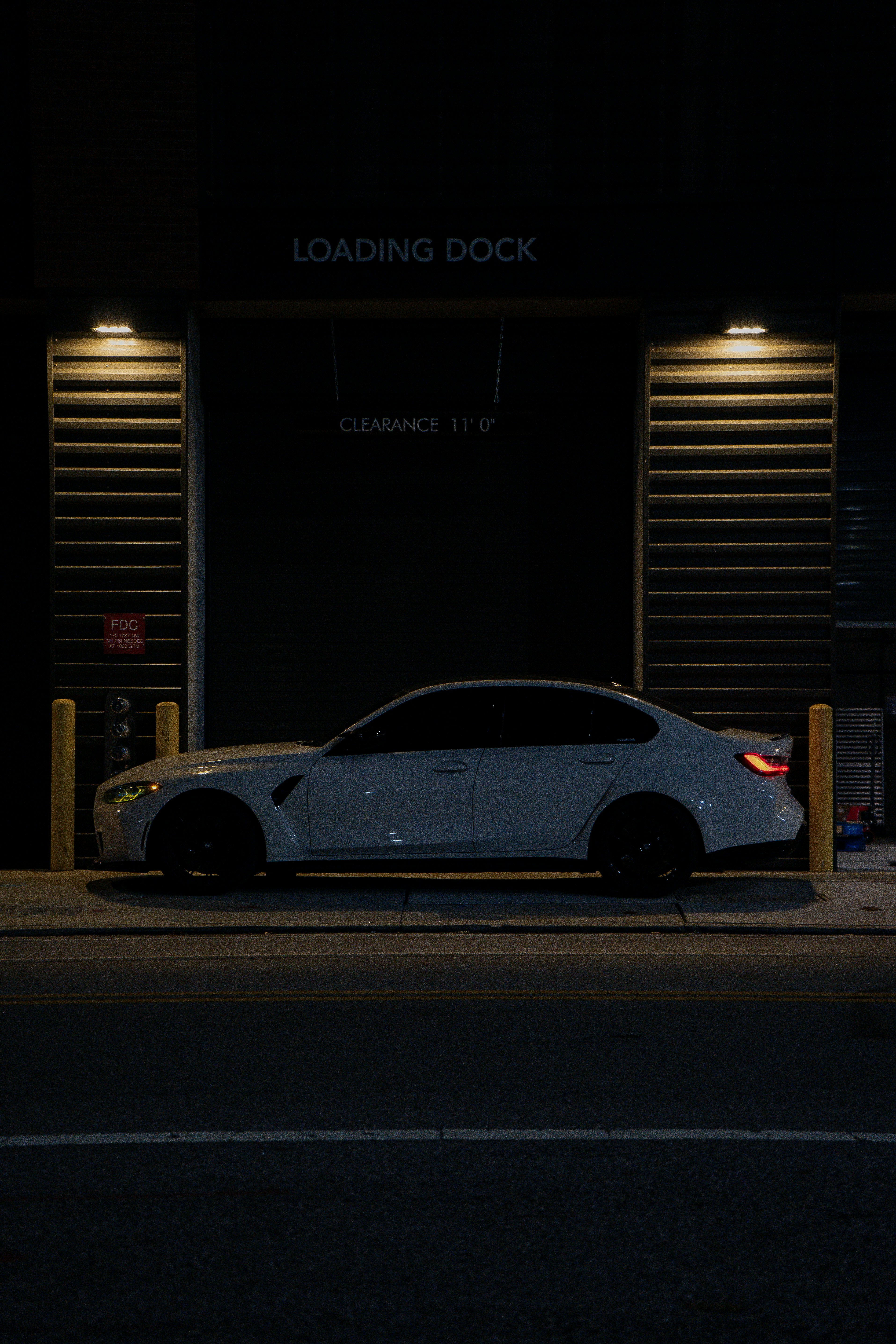 White sedan under storefront glow on a dim city street