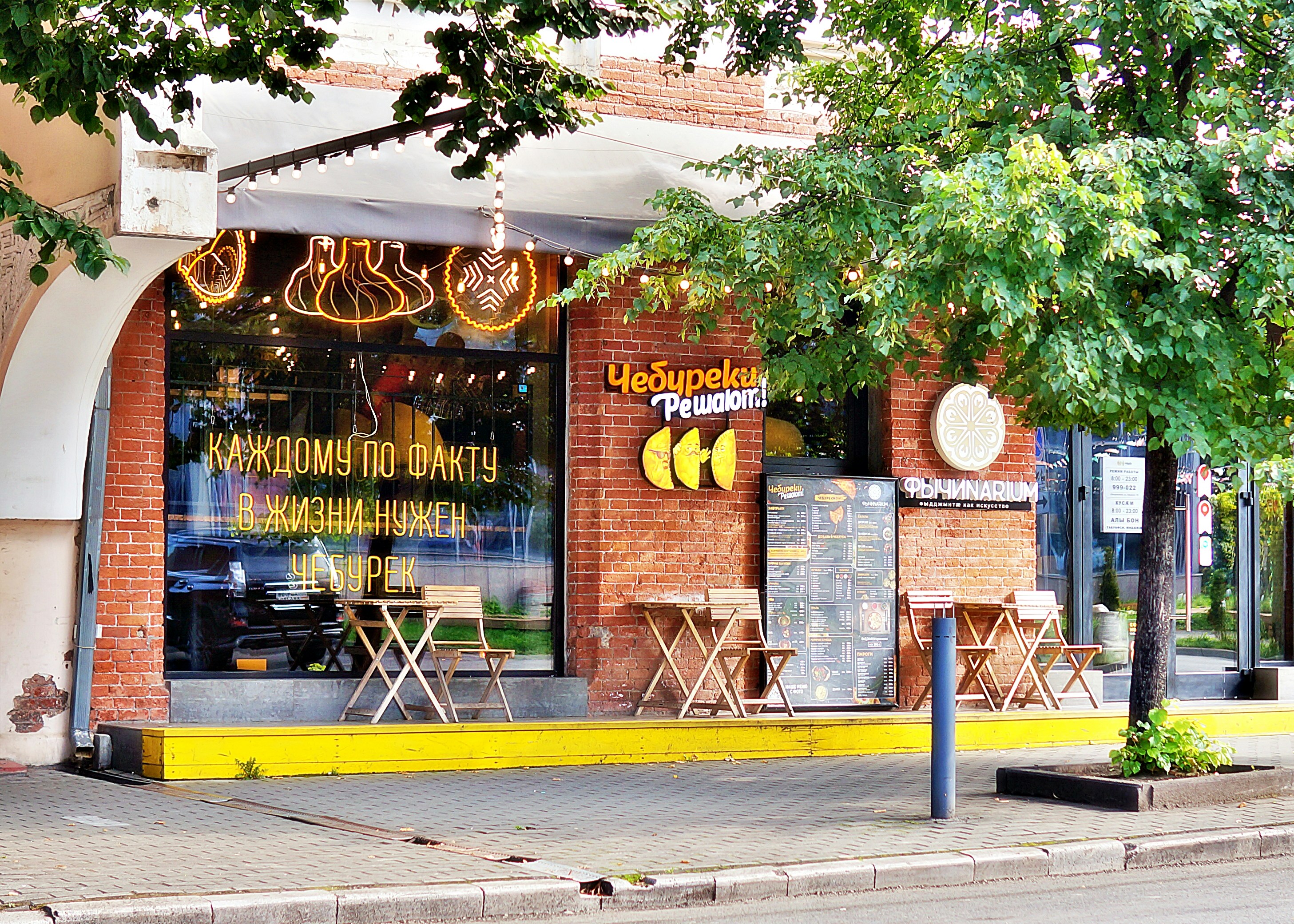 Cheburek Corner: Neon Signs, Brick Facade and Green Canopy