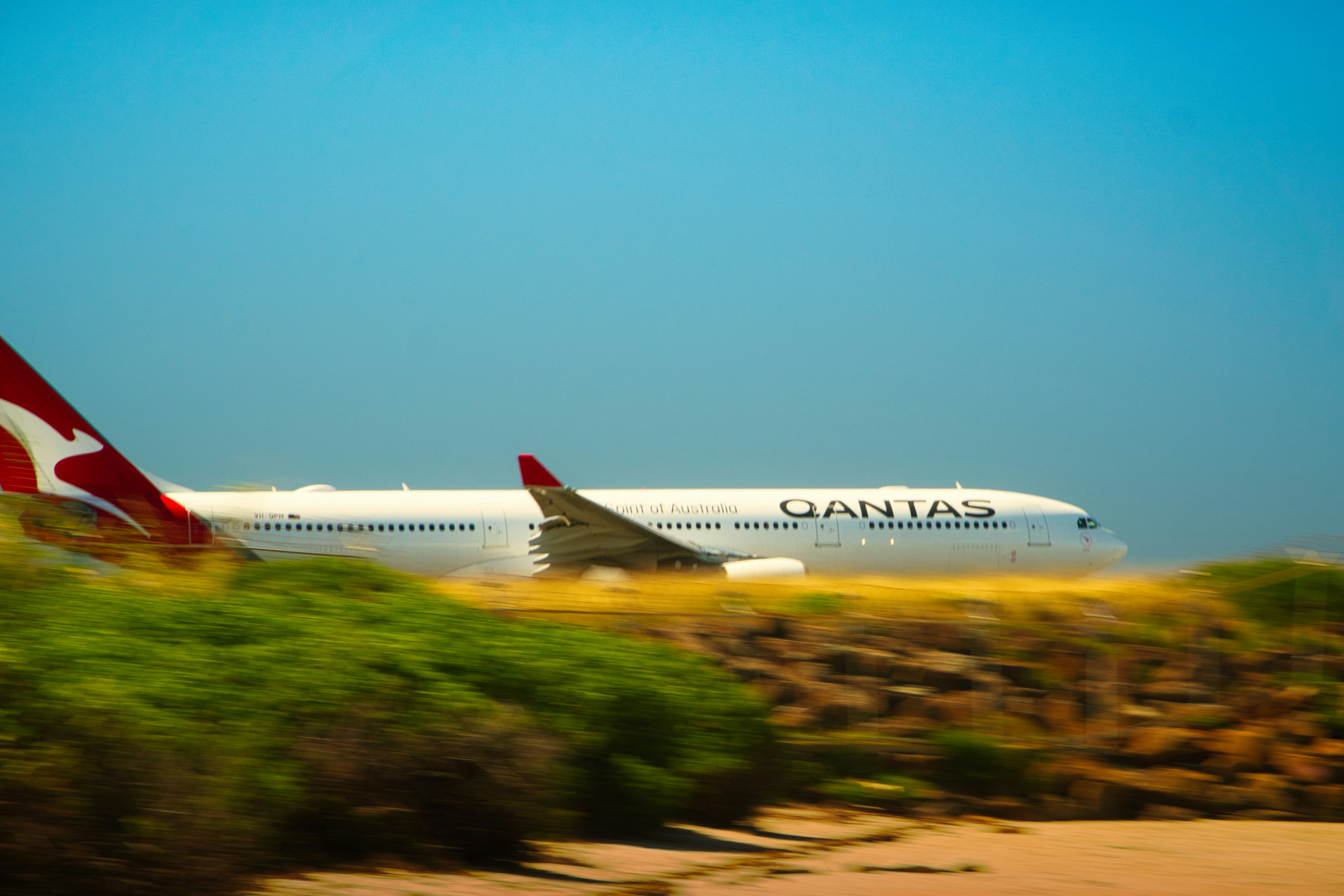 Qantas jet gliding through a sunlit scrub landscape