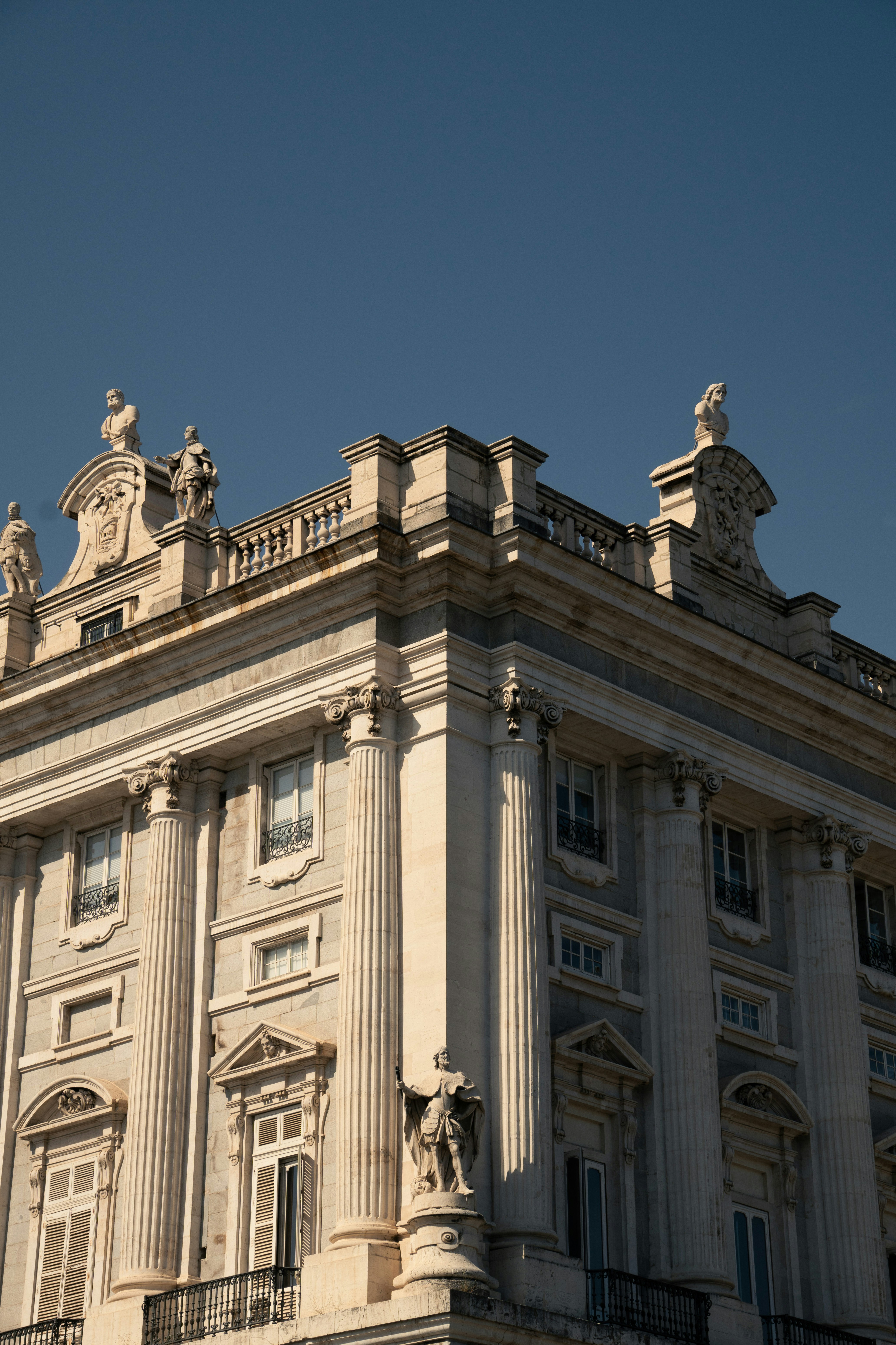 Classic institutional façade with statues and fluted columns under a deep blue sky, showcasing architectural detailing and sculptural elements.