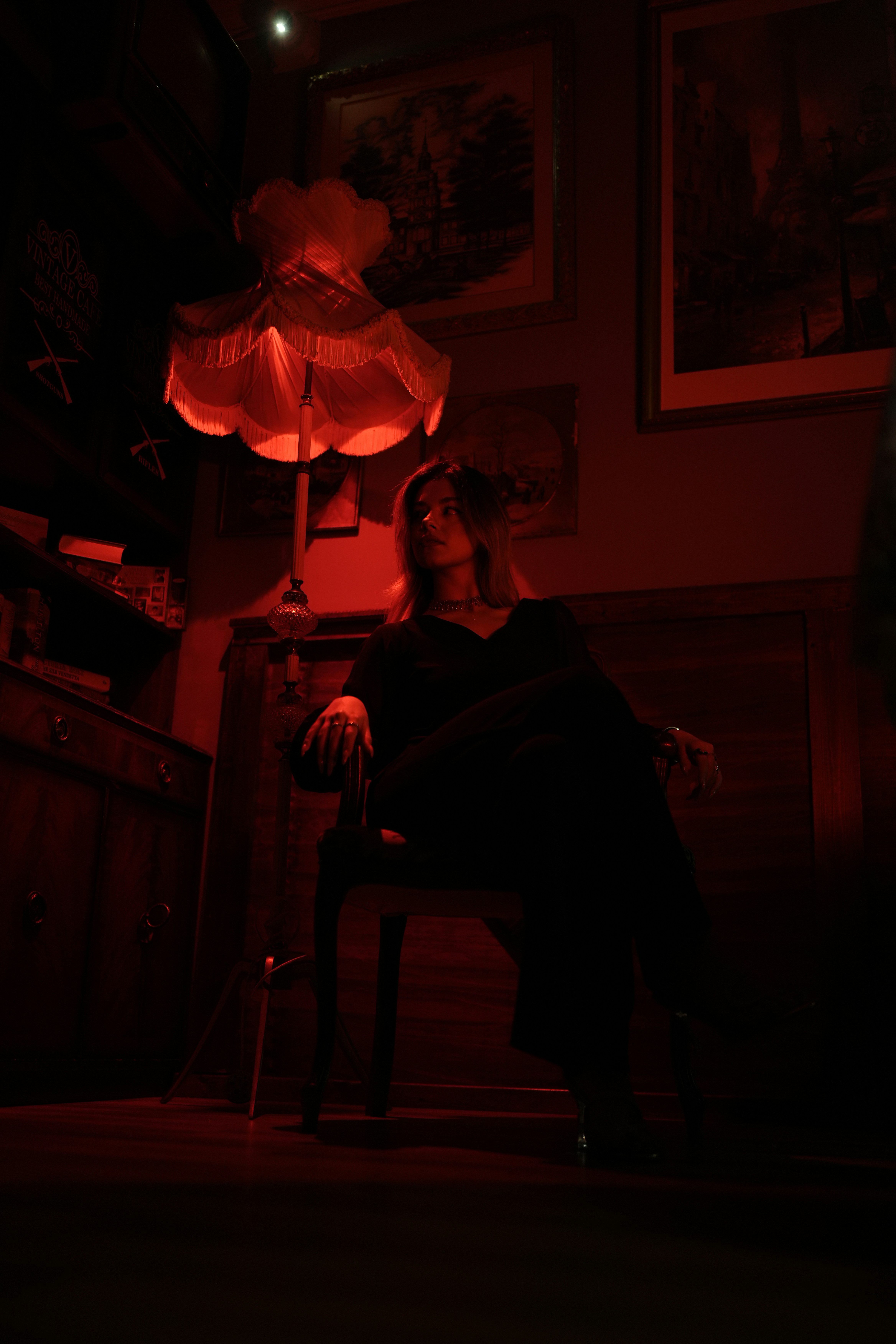 Shadowed lounge: a woman seated under a red lamp in a vintage room