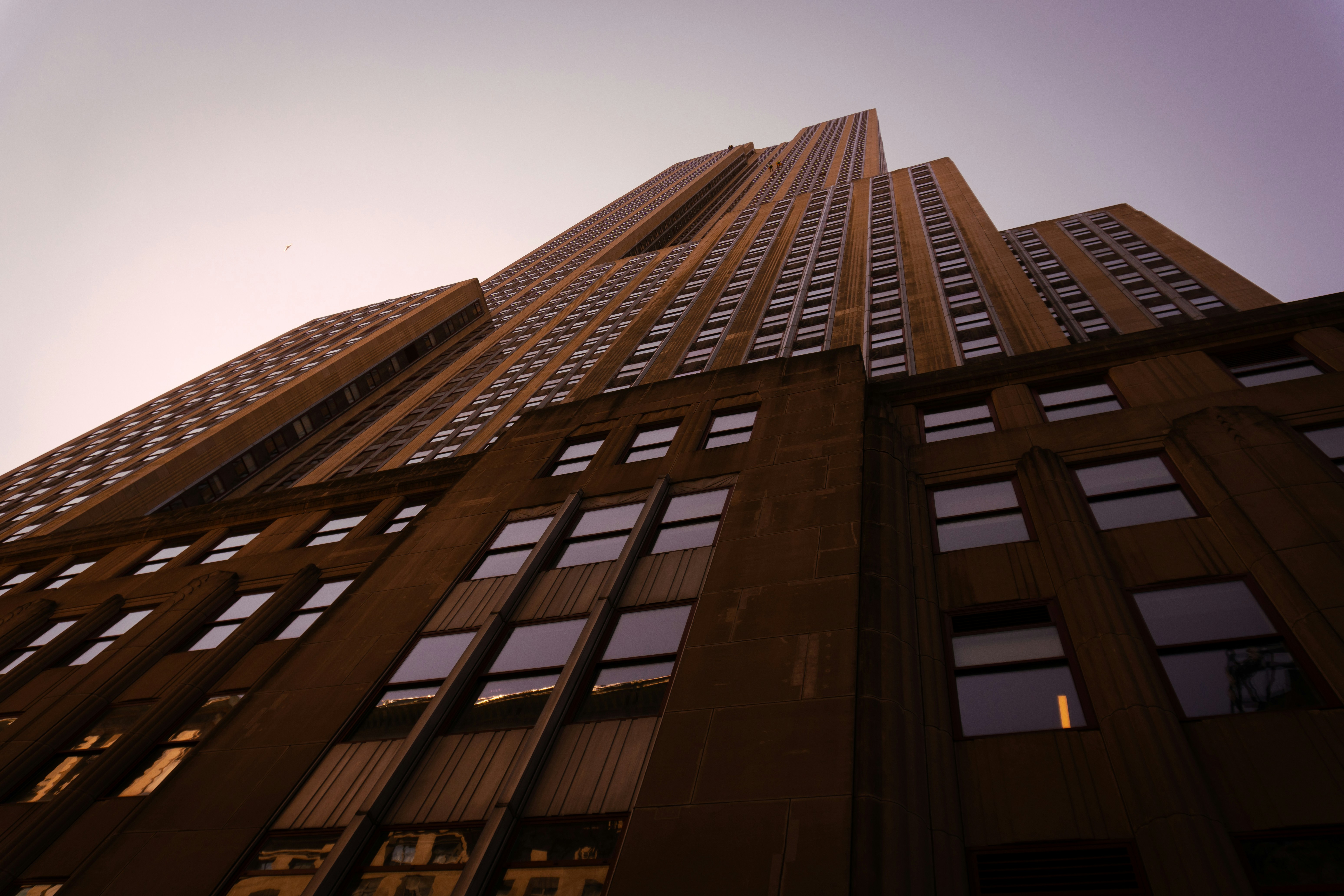 Vertical-angle view of a tall brick office building with numerous windows, taken from ground level looking up toward the peak, emphasizing architectural rhythm and converging perspective.