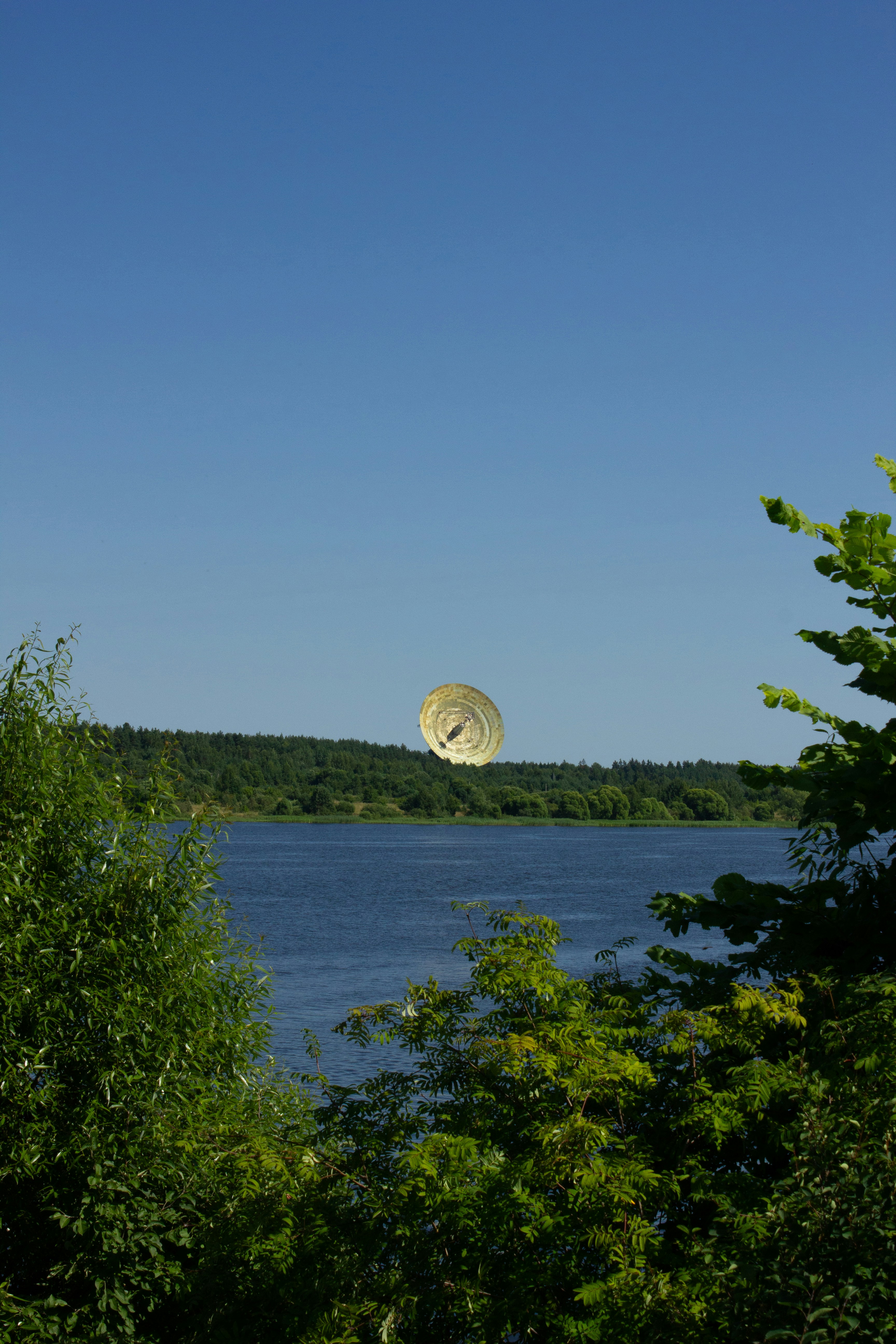 Floating beacon over the river: a distant paraglider against a clear sky