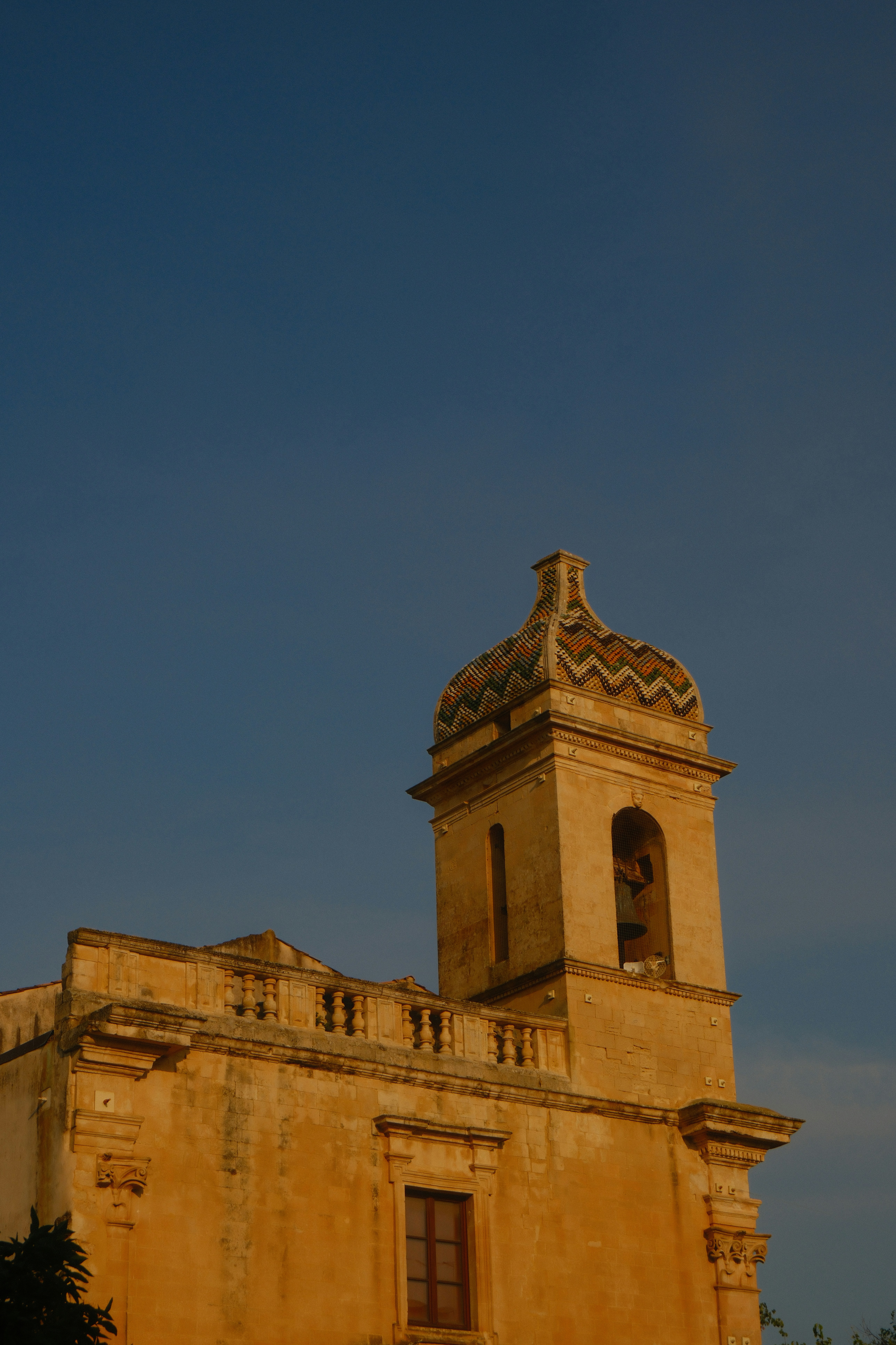 A sunlit bell tower rises from warm stone against a clear evening sky