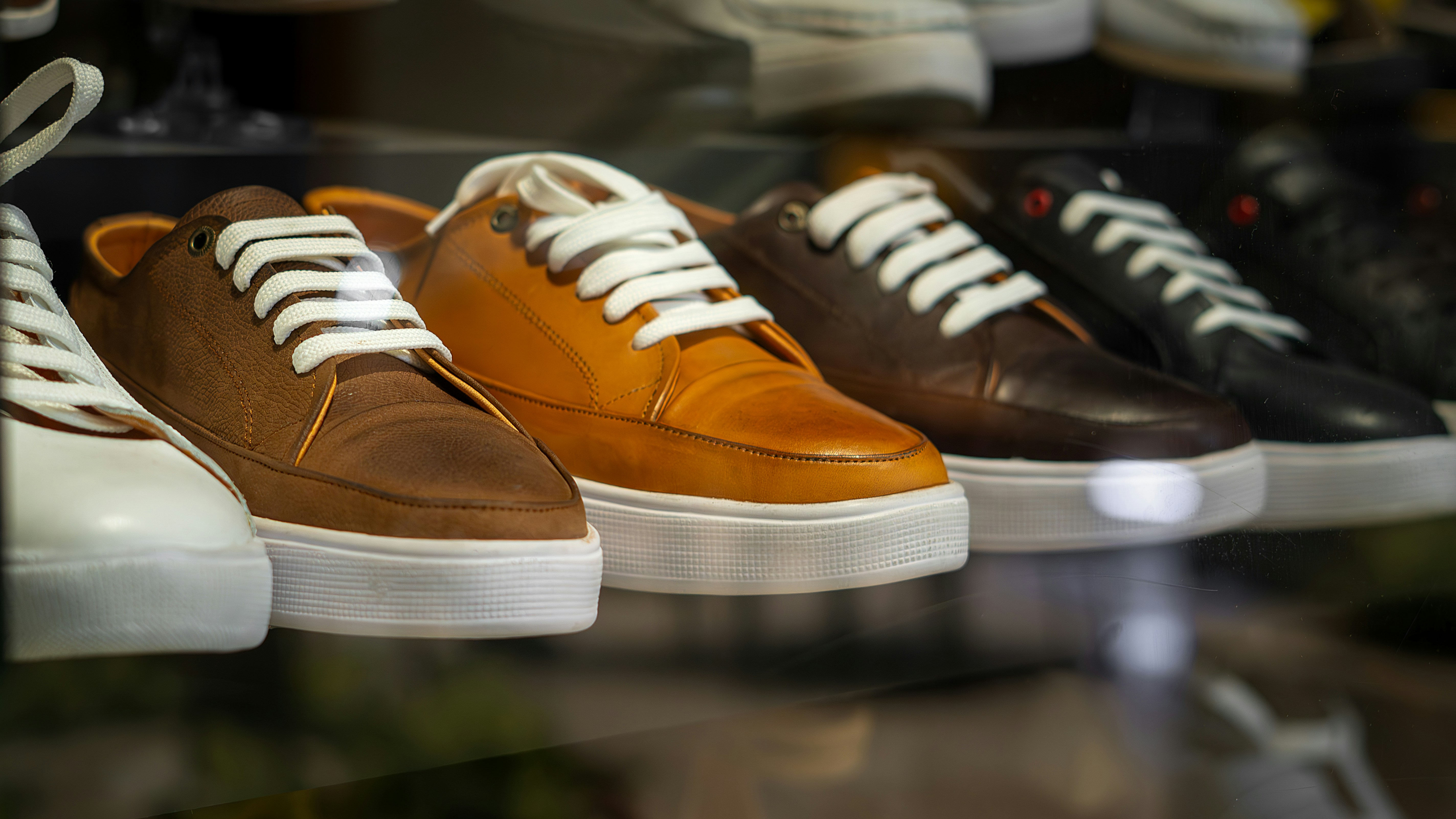 Warm-toned sneakers aligned along a glass shelf, with a shallow depth of field highlighting the front row while others fade; a retail display shot.