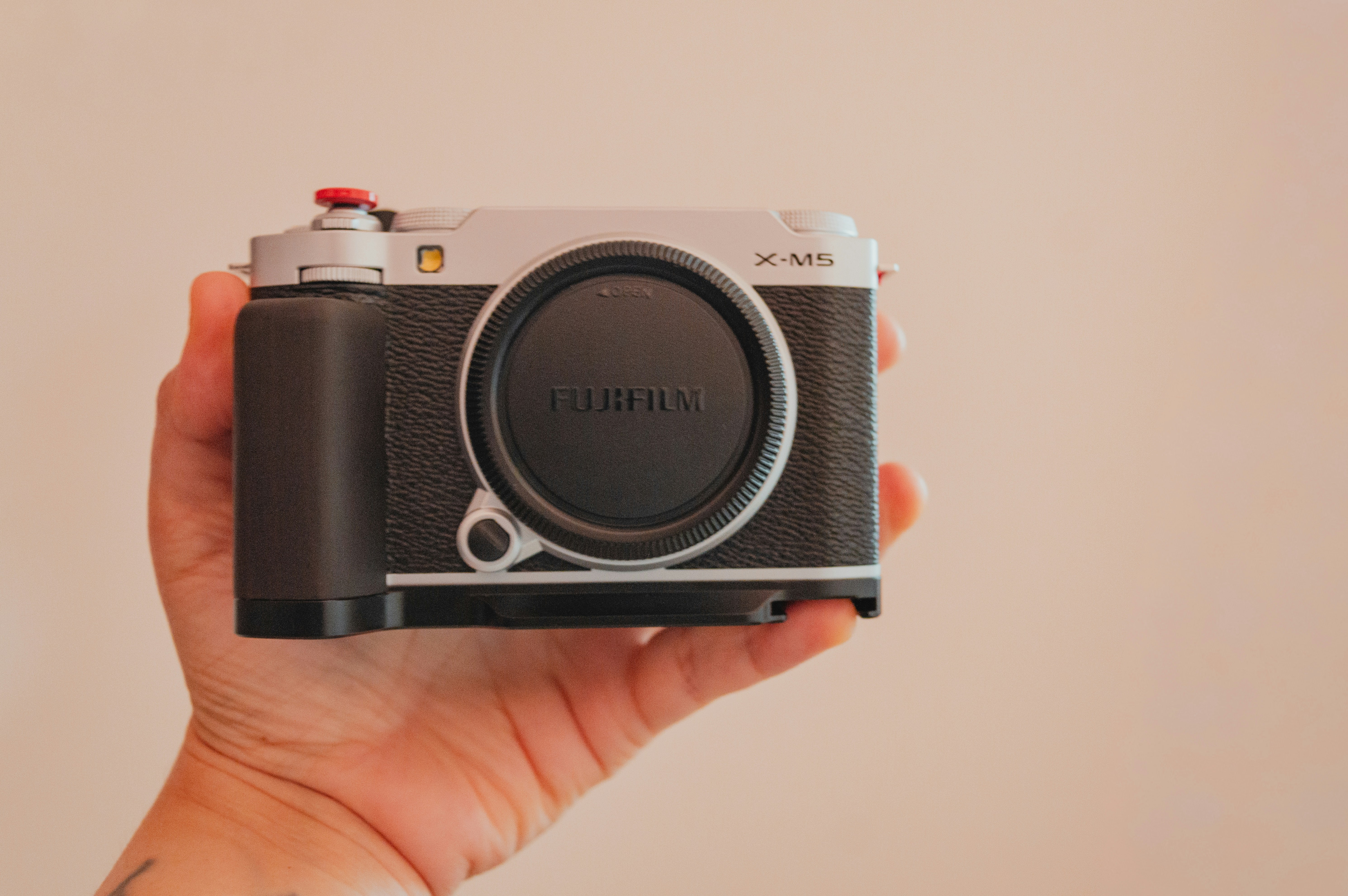 Compact mirrorless Fuji X-MS in hand shows clean lines and tactile metal finish with a soft, warm background.